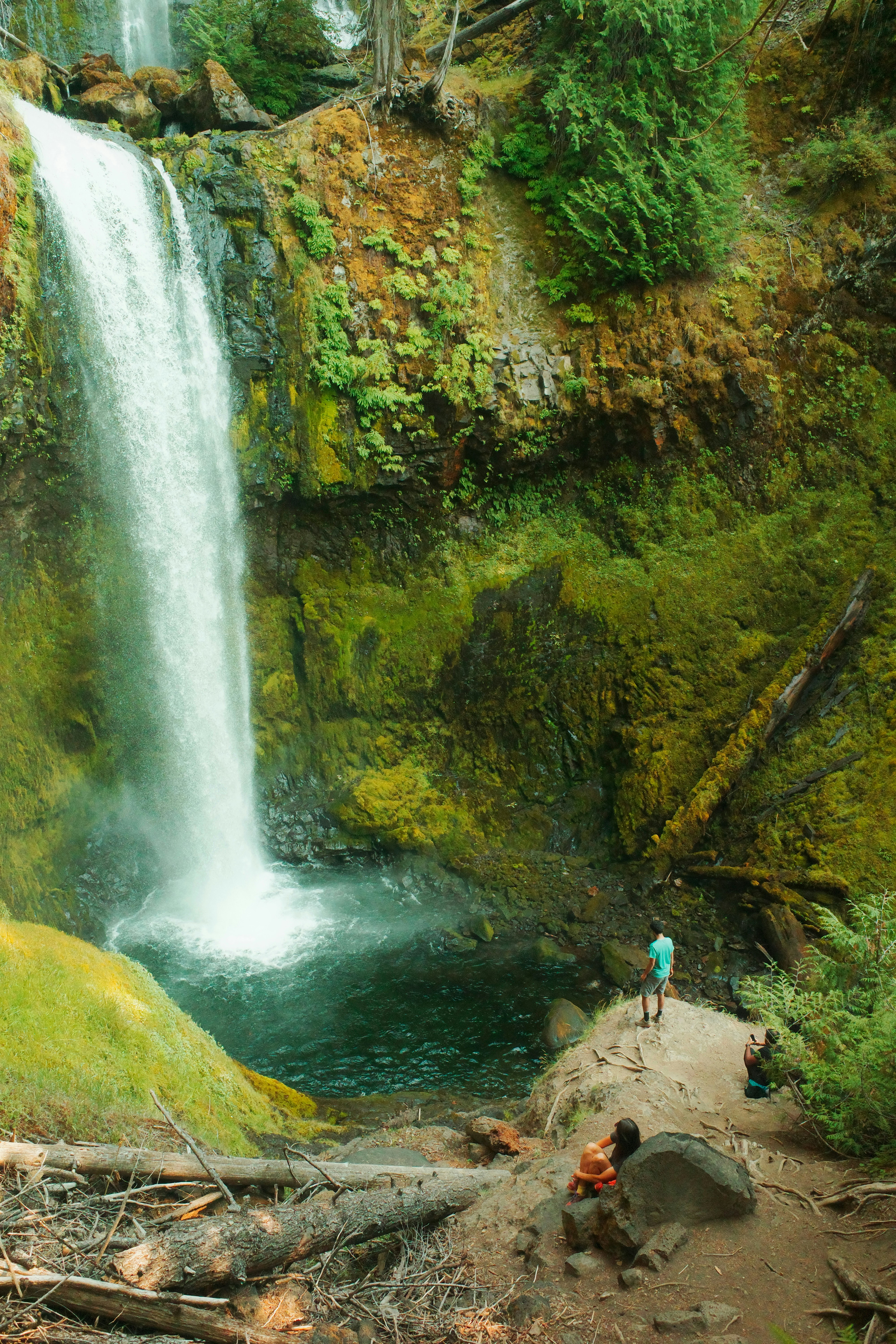 Misty Cascade at the Edge: Explorers at the Base of a Verdant Fall