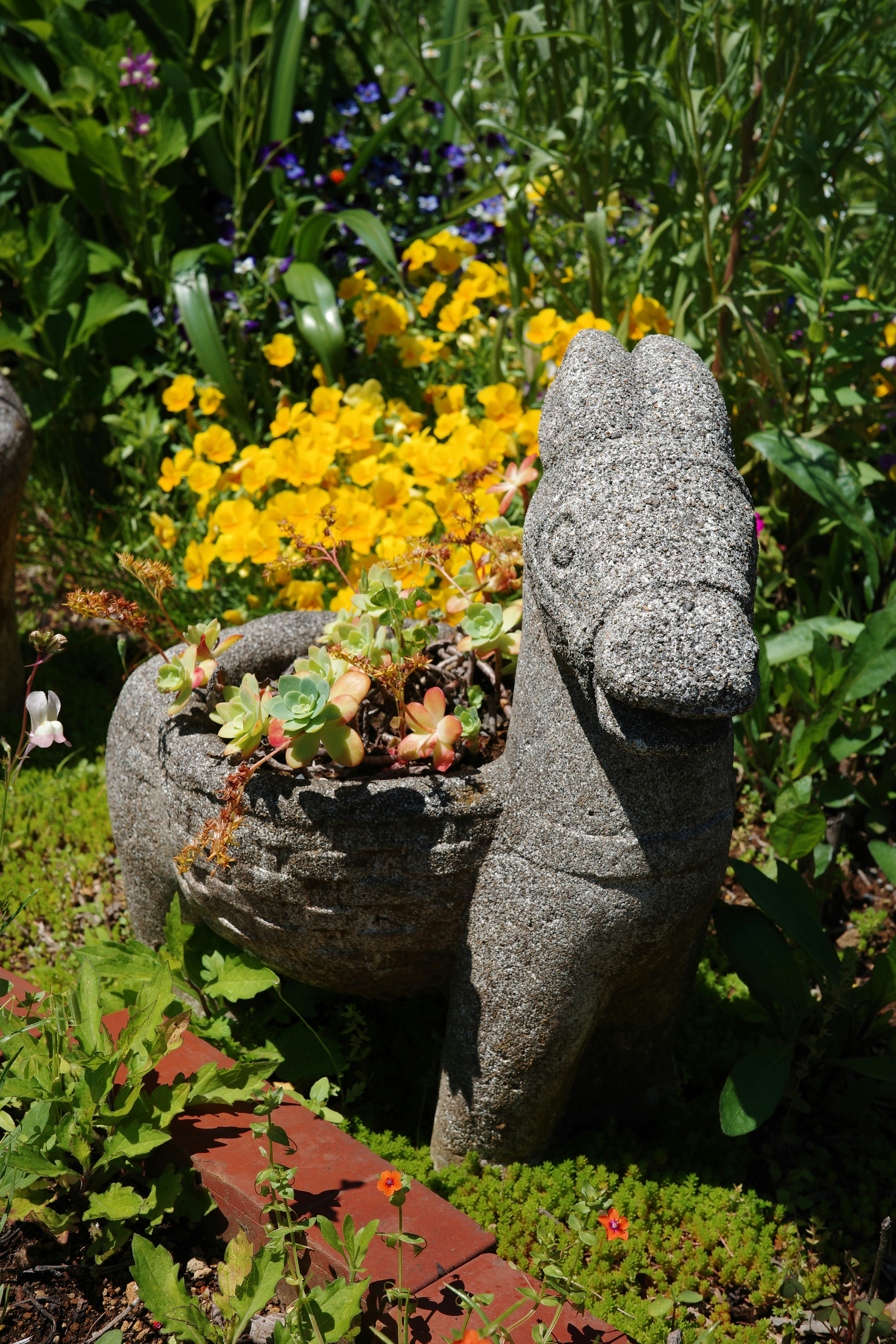 Stone goat planter amid a blooming garden