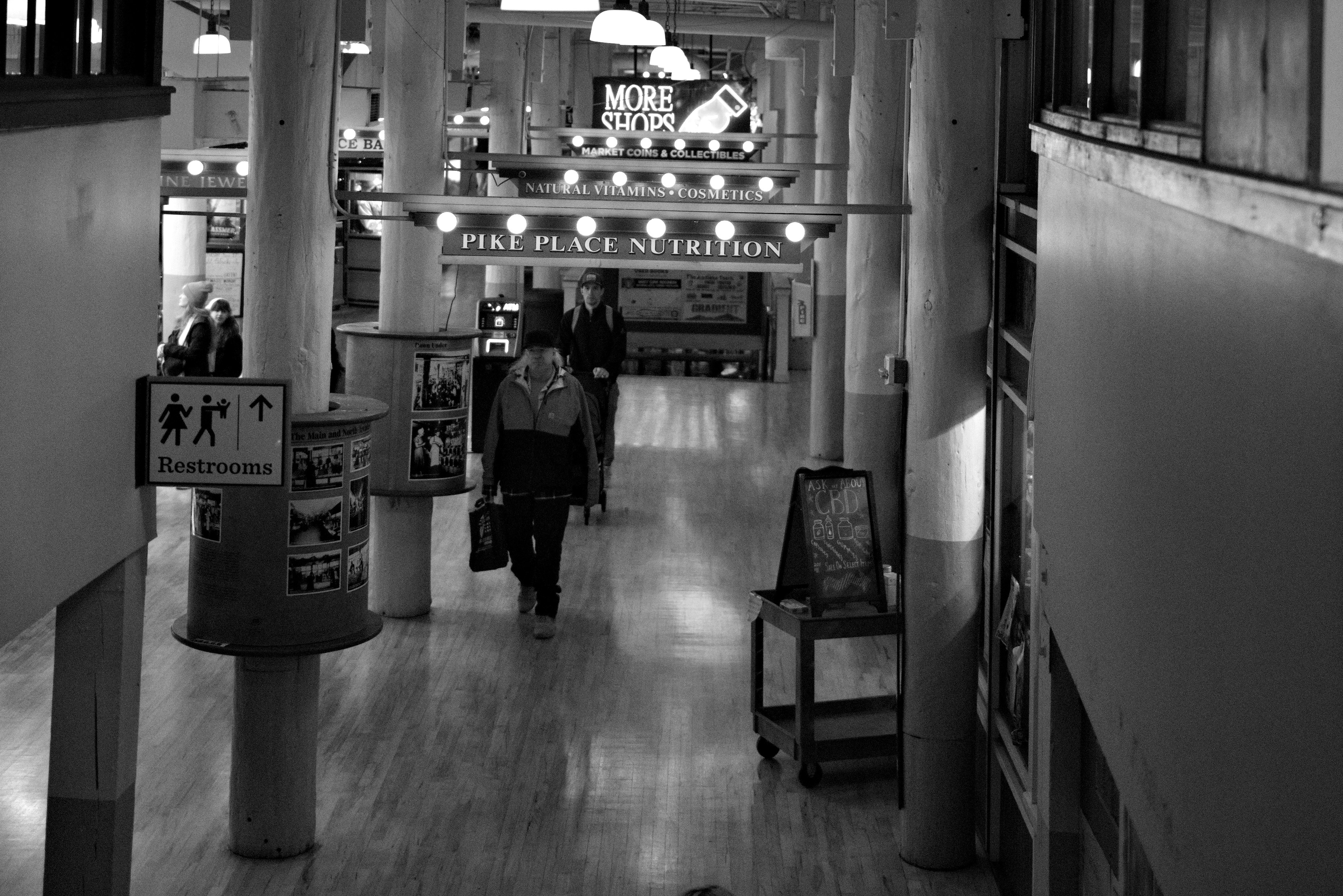 Mid-Aisle Quiet: Shoppers Pass a Dim Corridor under Painted Beams