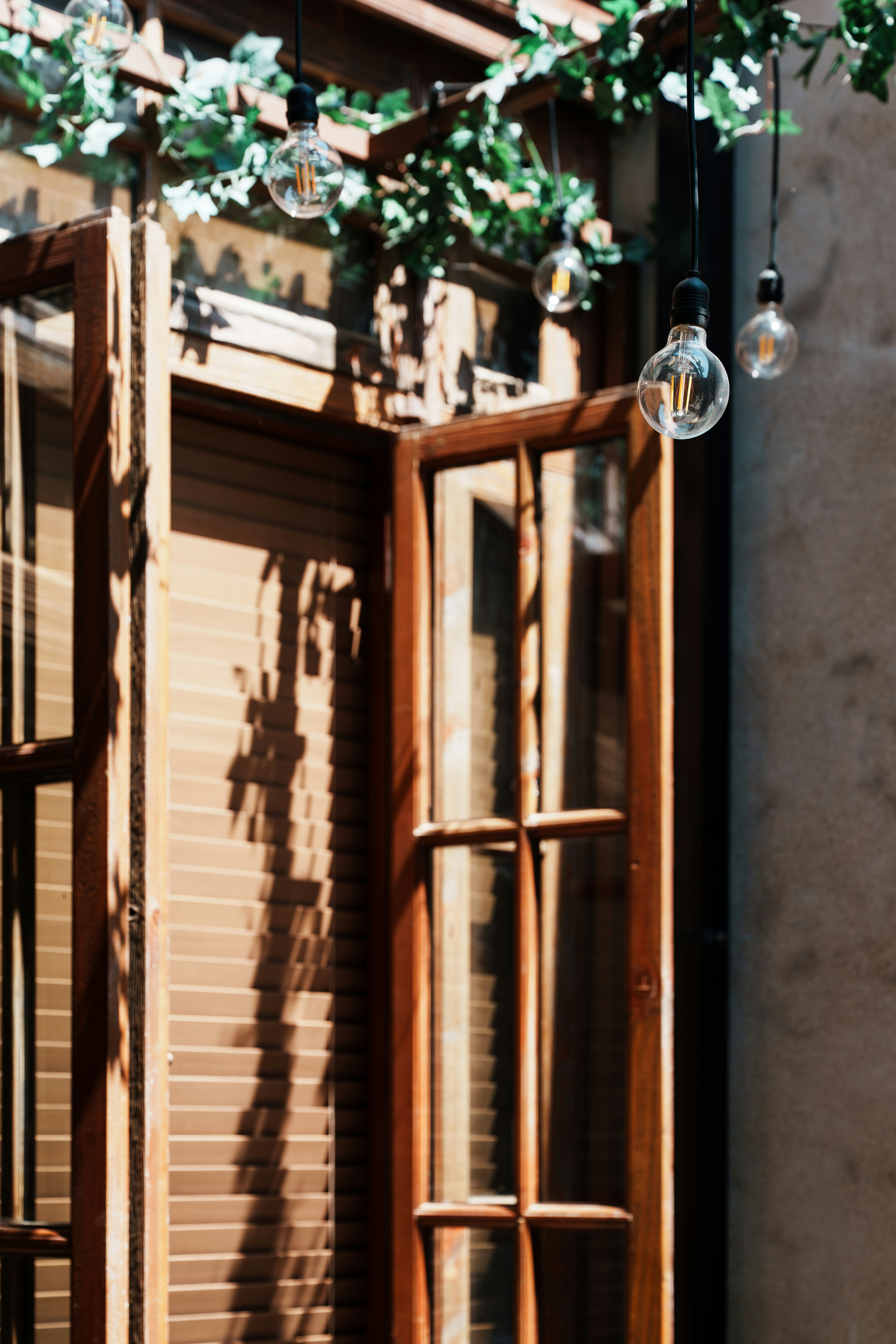 Sunlit Courtyard Glass: Warm Wood and Hanging Bulbs