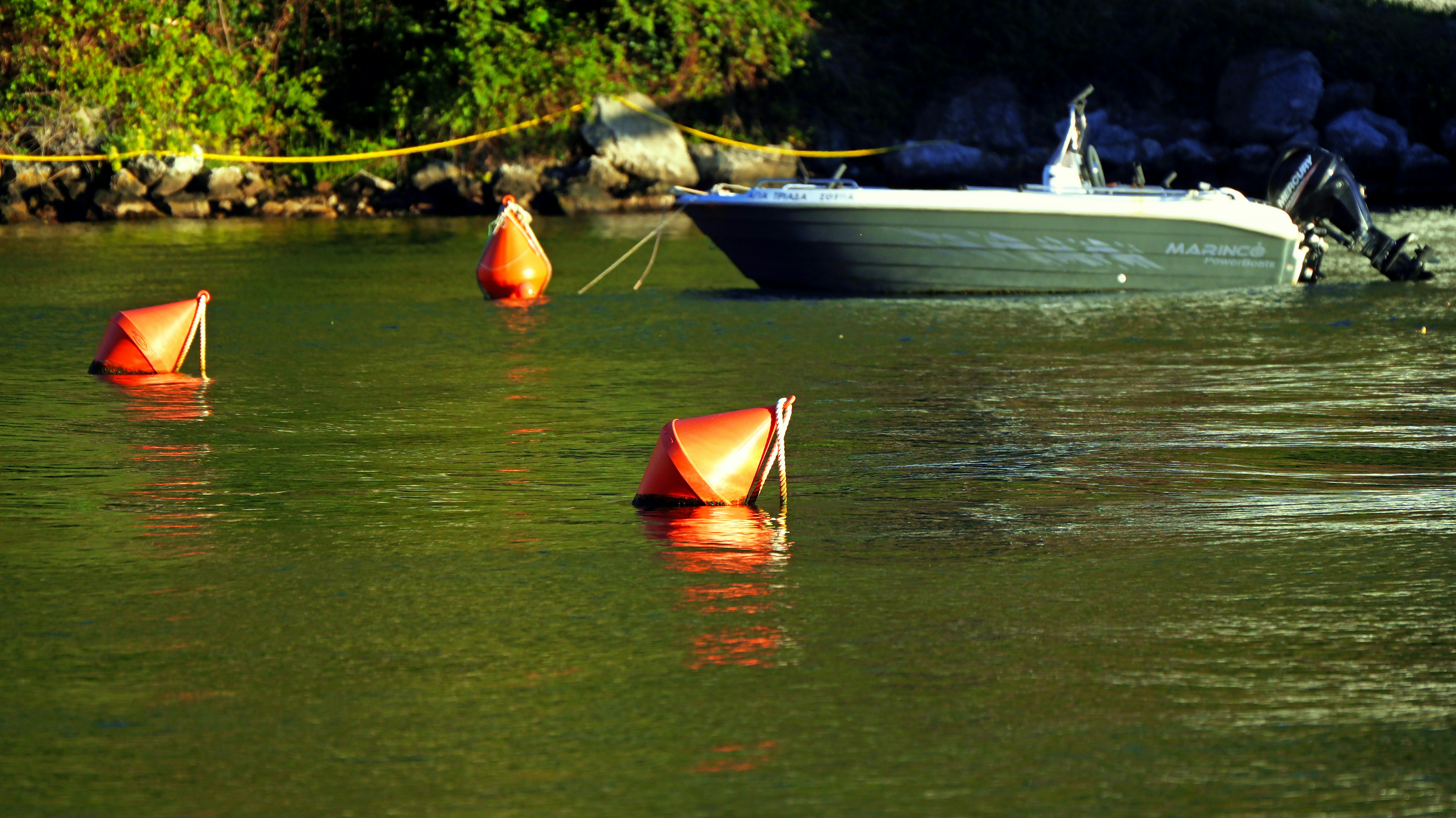 Sleek boat anchored near a calm shoreline while buoys drift in the foreground