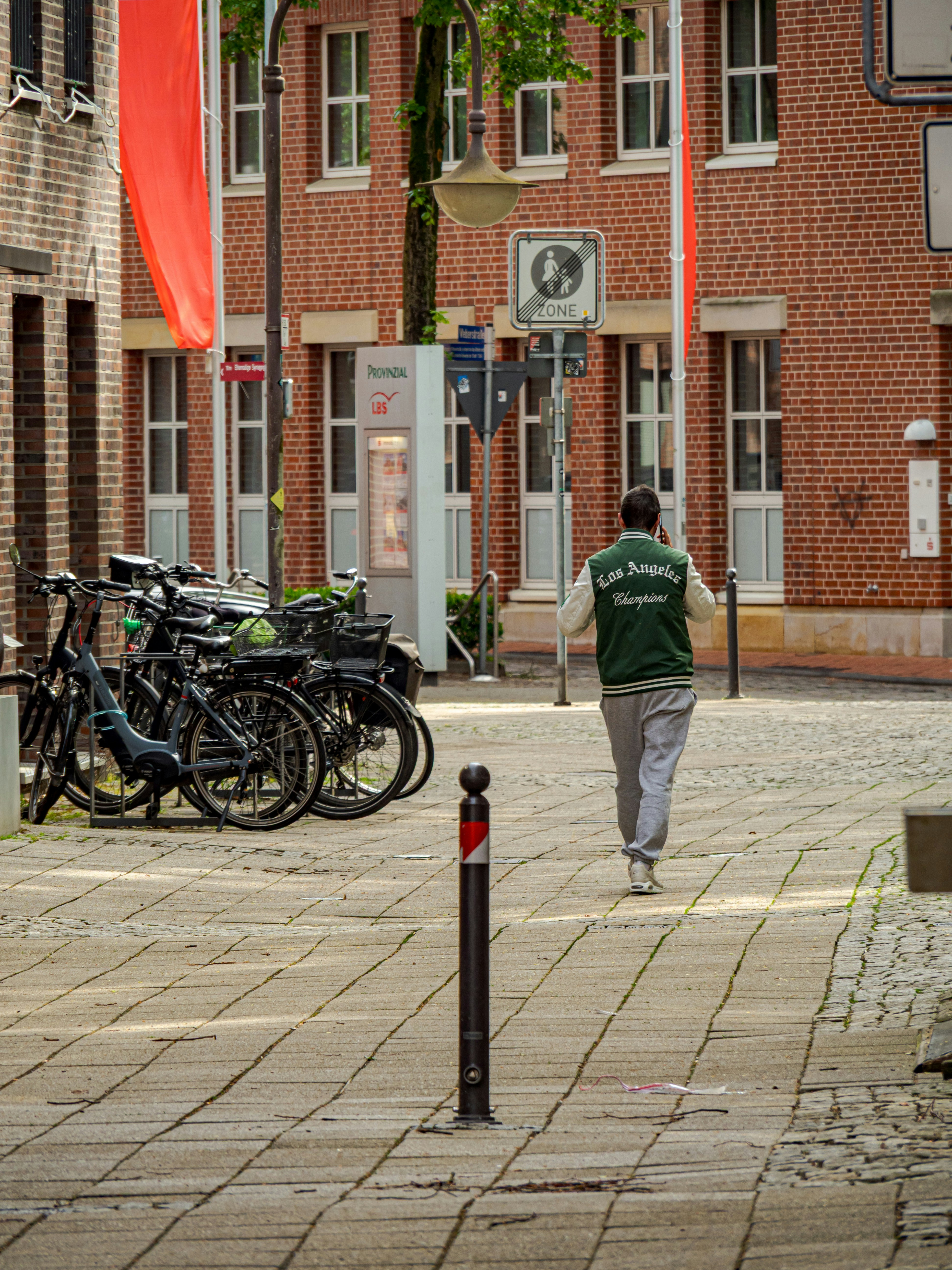 Man in a green varsity jacket walking away in a quiet cobbled street lined with bicycles