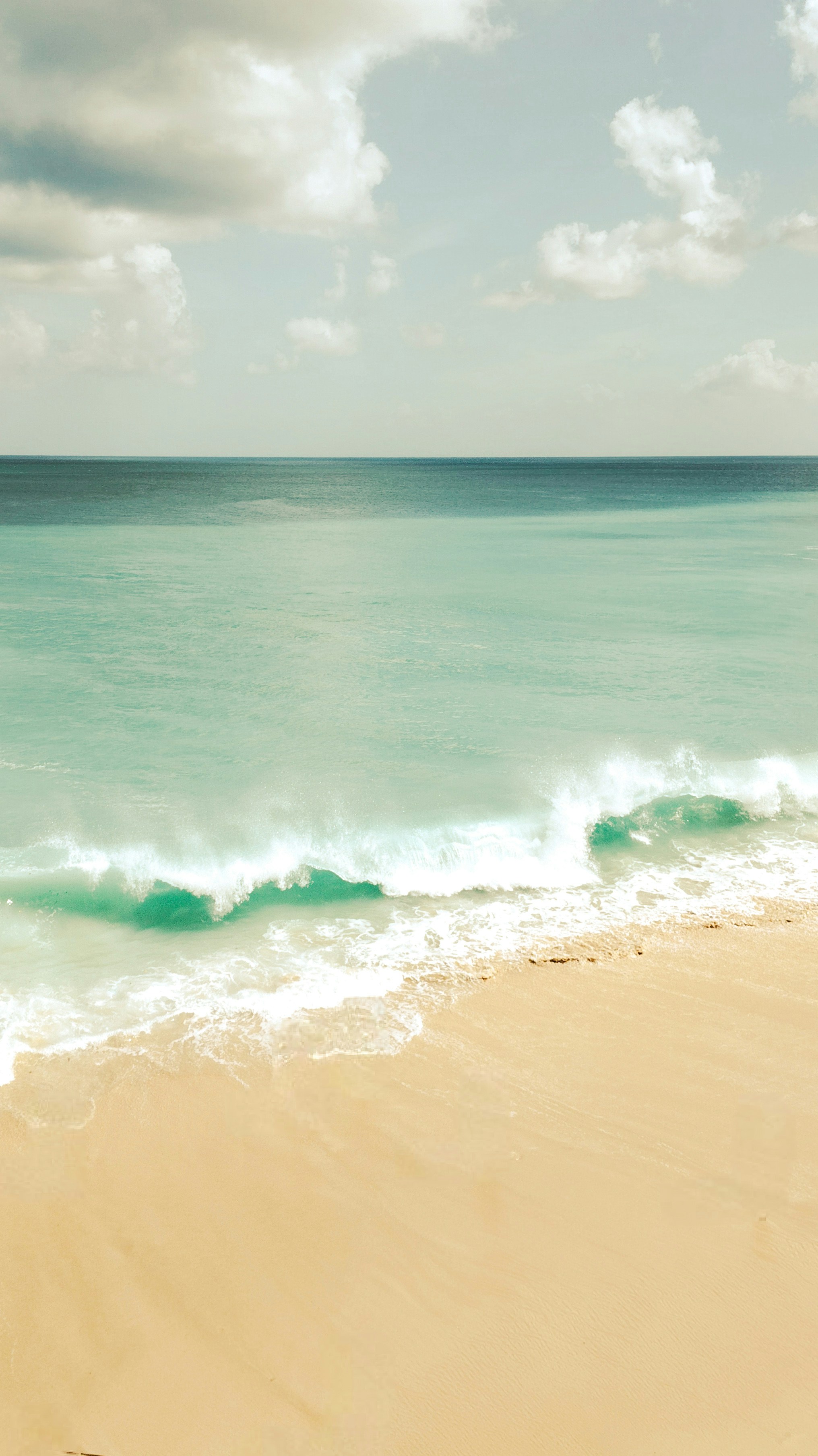 A gentle wave washes onto a sandy beach under clouds.