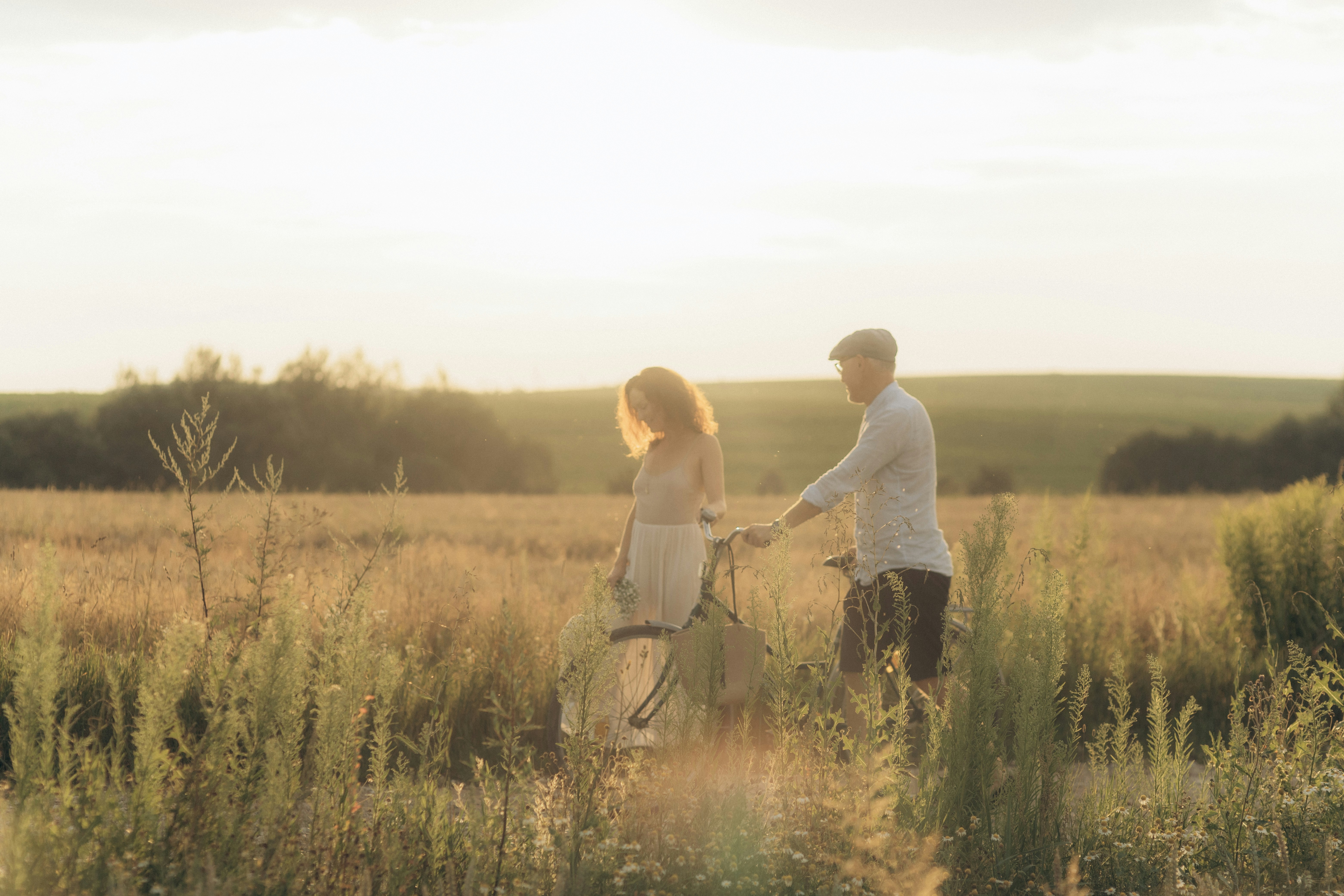 Golden Hour Stroll: A Couple on a Sunlit Field Bicycle Ride