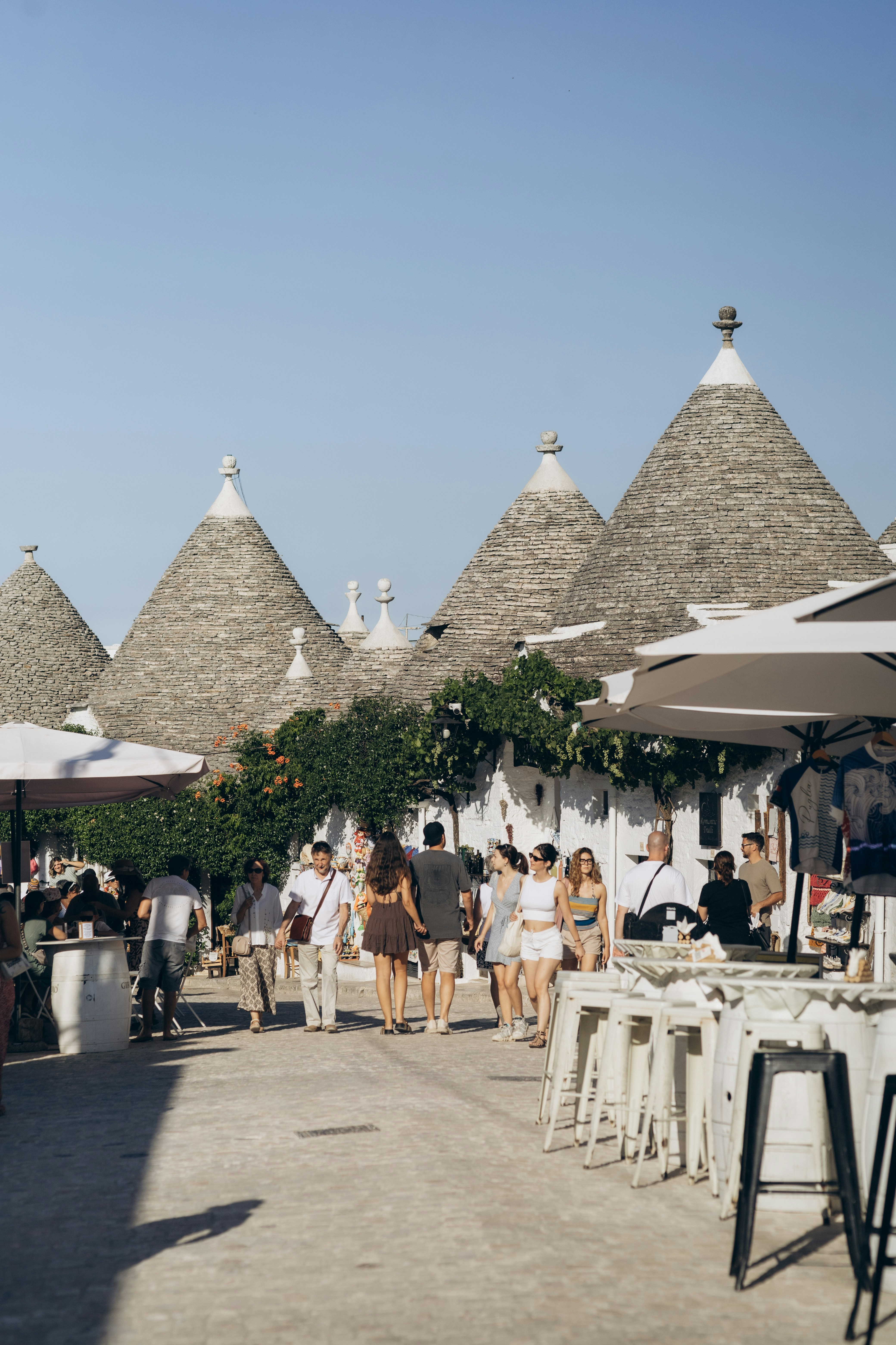 Sunny Trulli Alley: People Stroll Under Cone Roofed Towers