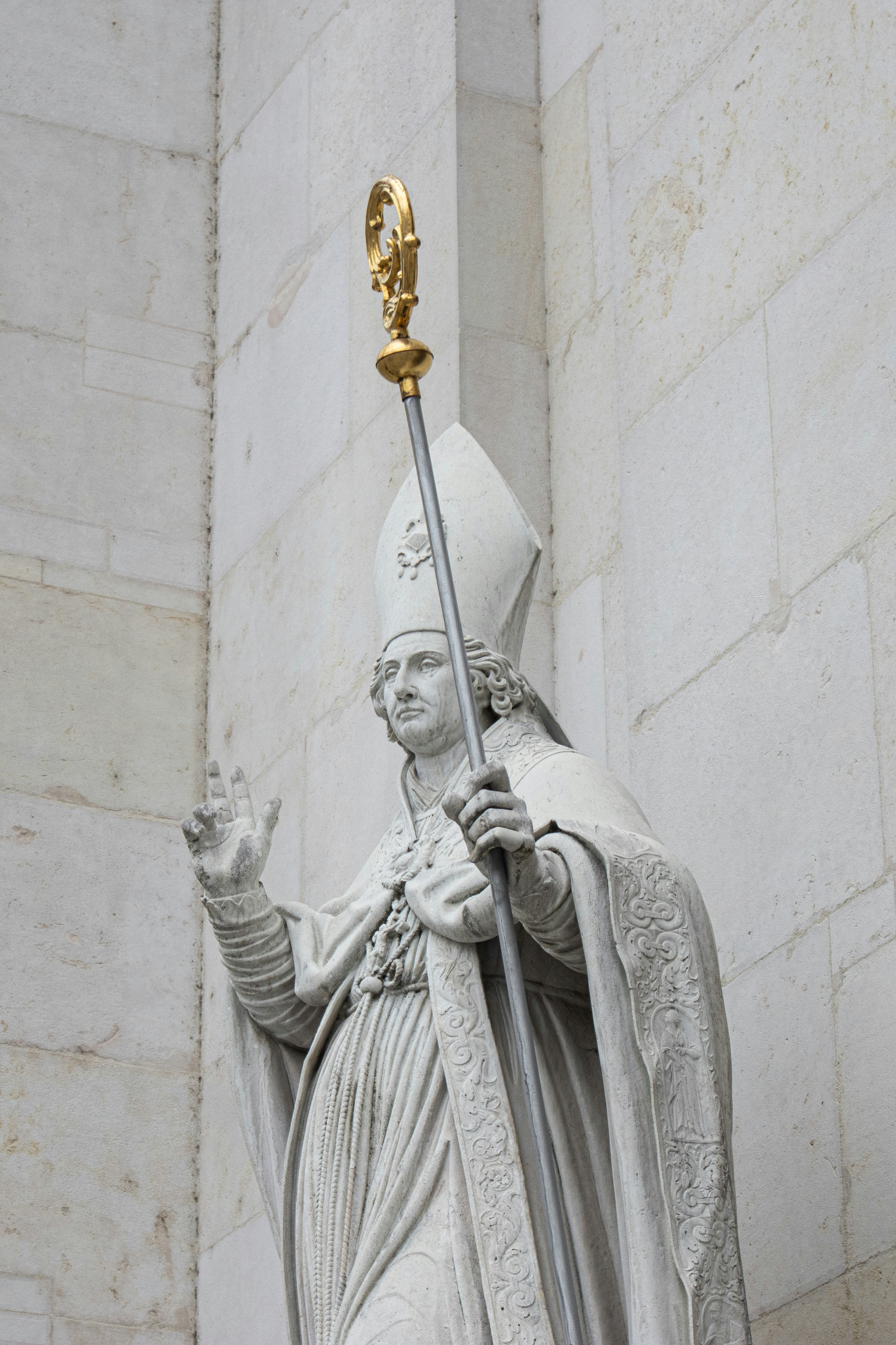 Stone Bishop Holds a Golden Crosier Above a Looming Cathedral Wall