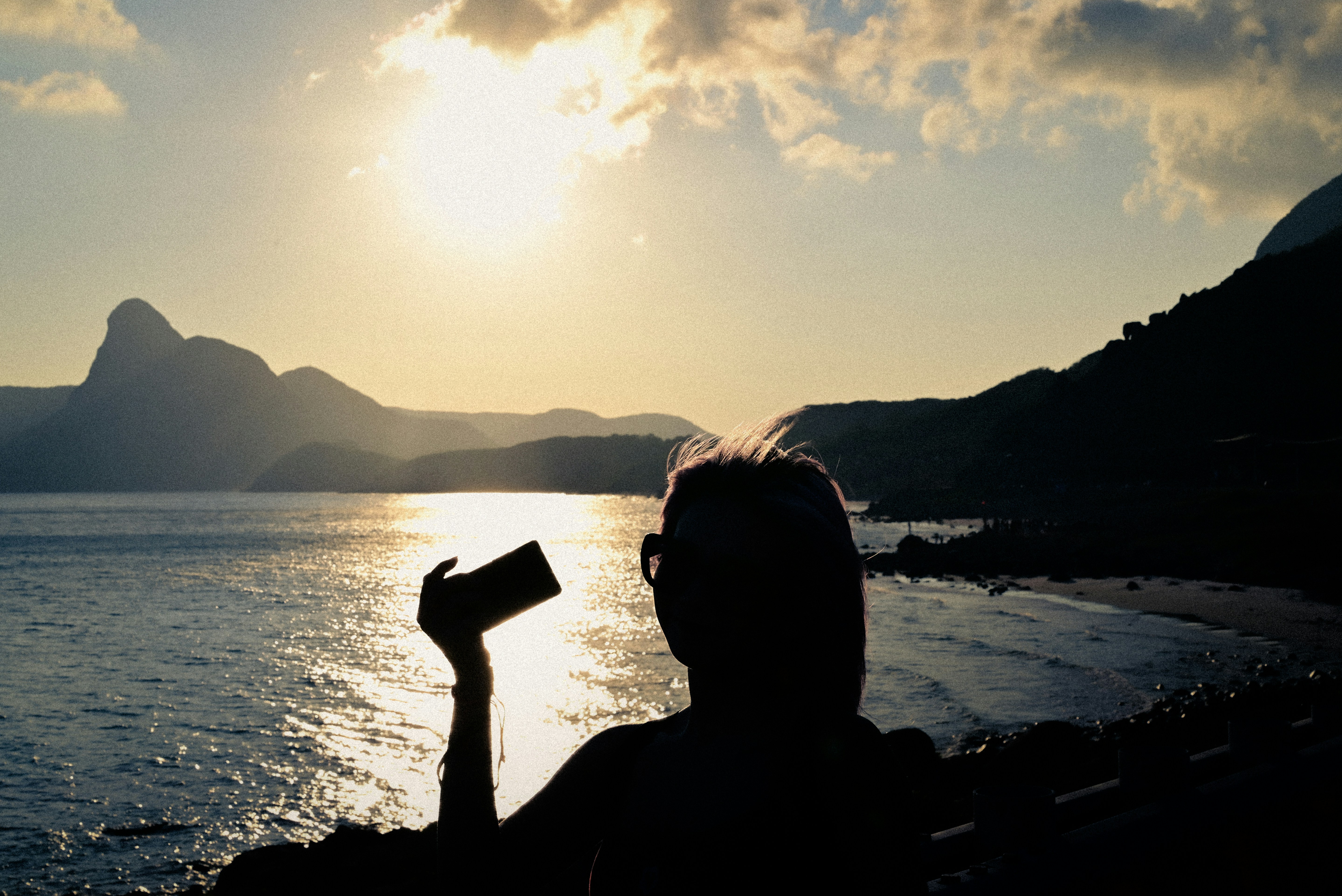Silhouette at Sunset: A Person Holding a Phone Against Coastal Backdrop