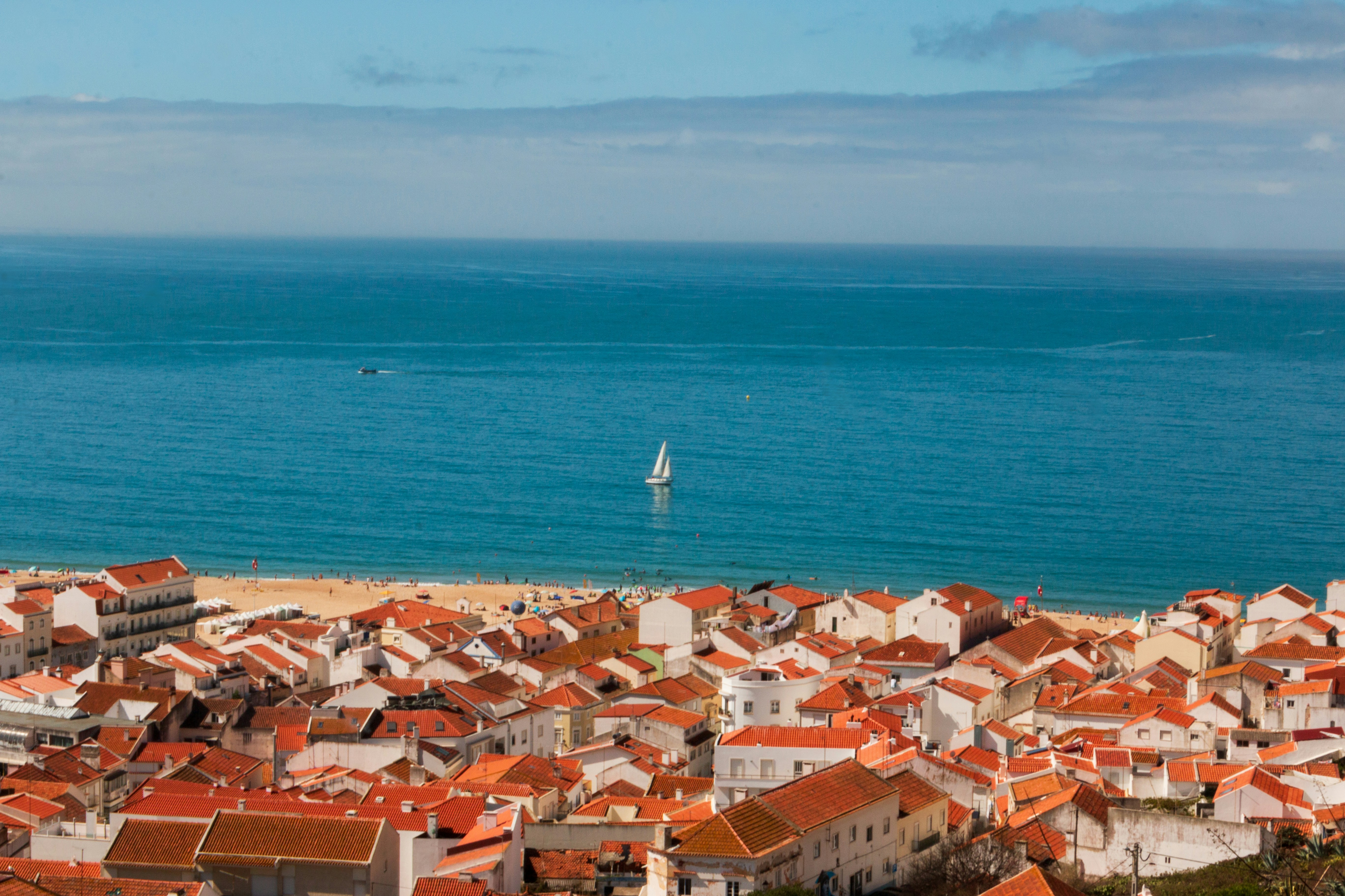 Coastal Village Rooftops Leading to a Sailboat on a Calm Horizon