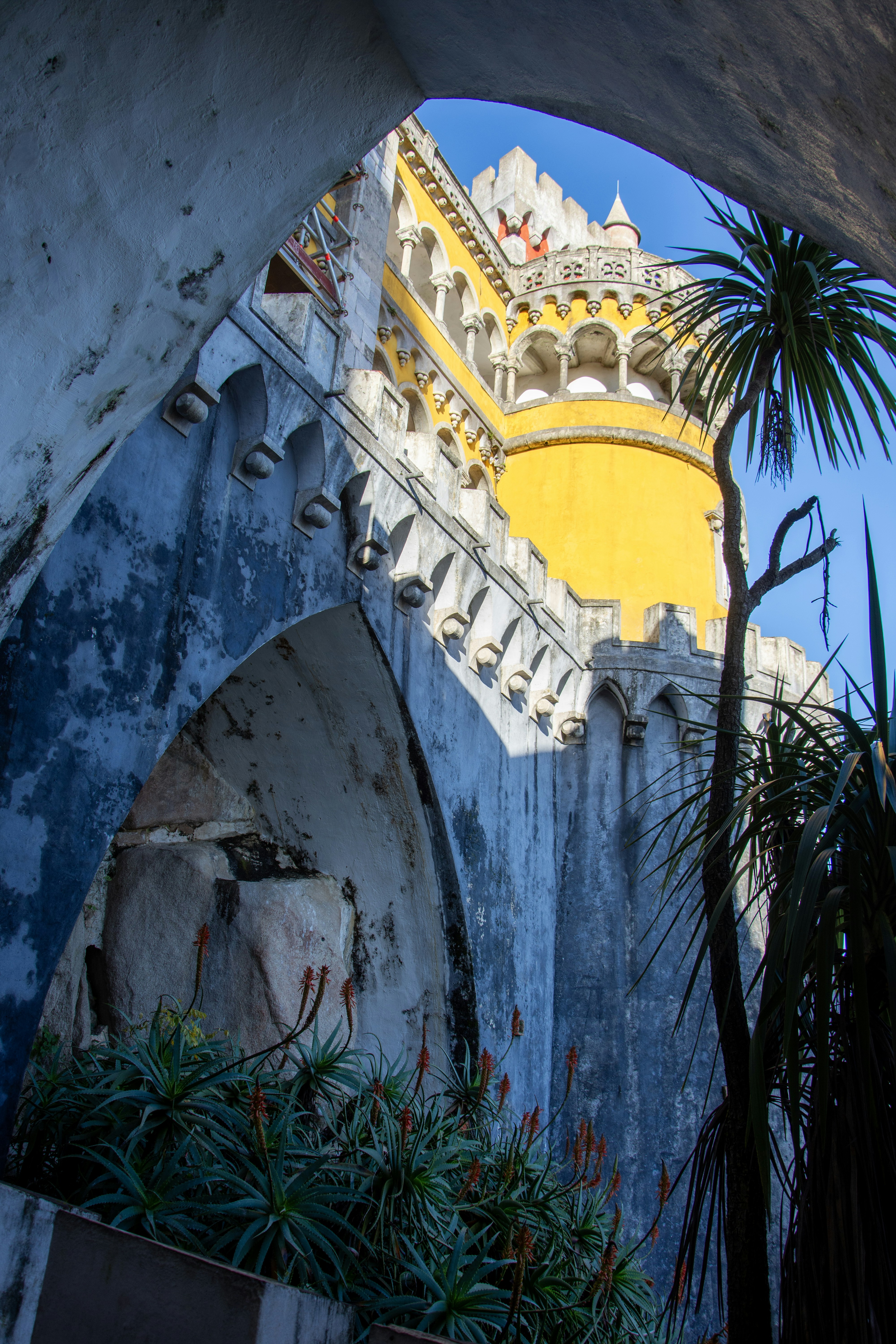A vibrant yellow castle with arched walkways and greenery.