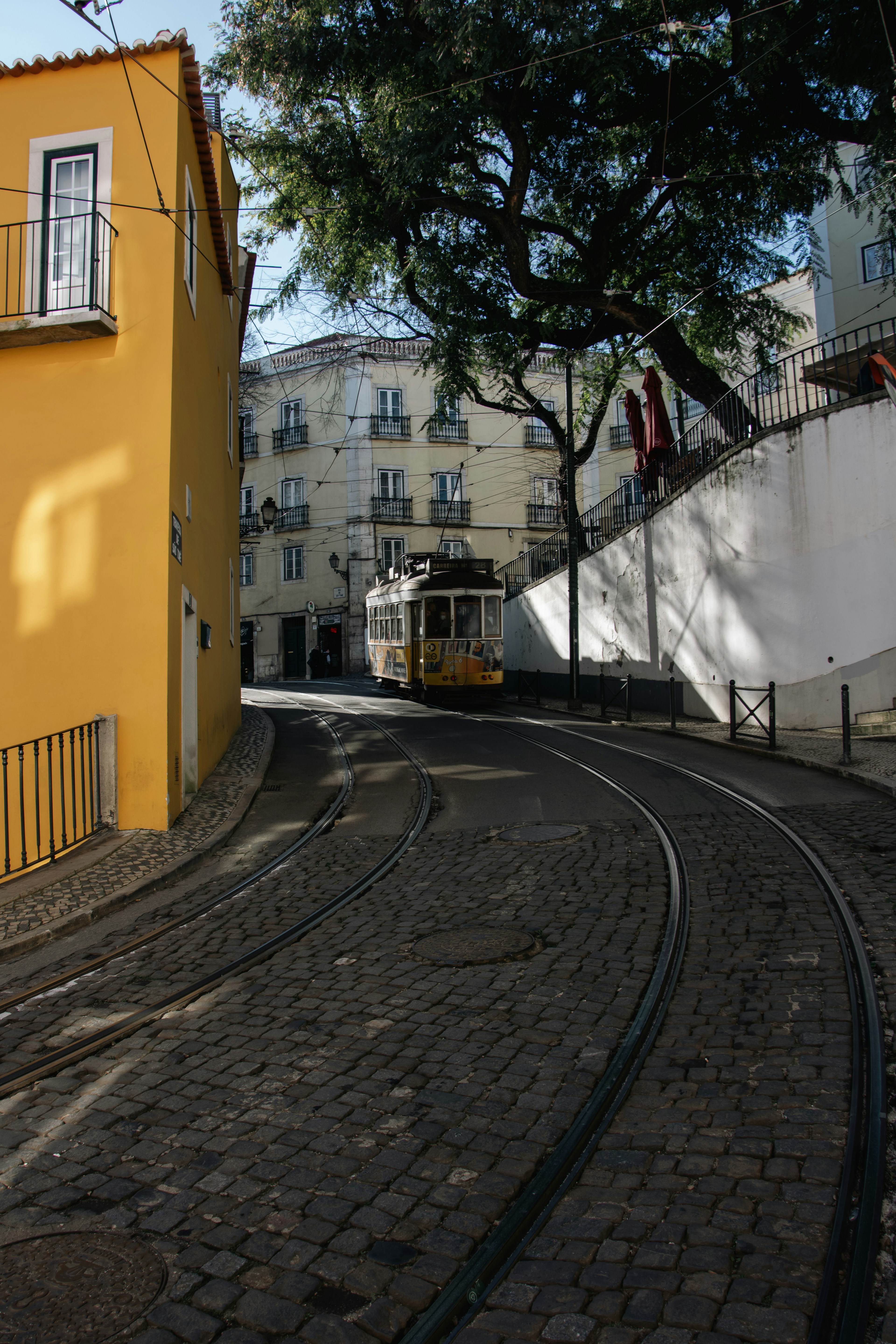 Yellow Arc: A Tram Wends Through a Cobbled Lisbon Street