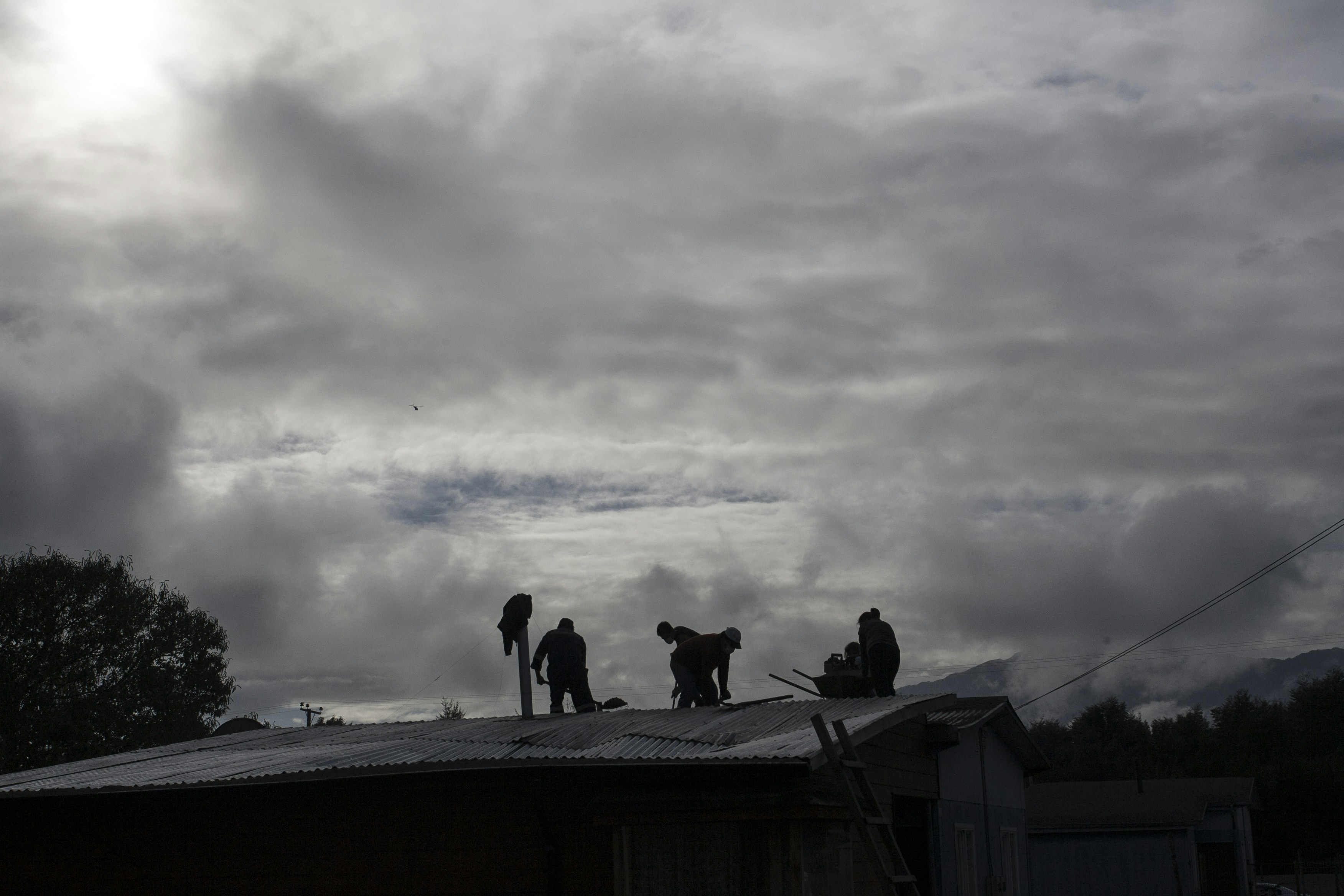 Rooftop silhouettes at dusk: a small crew on a corrugated shelter