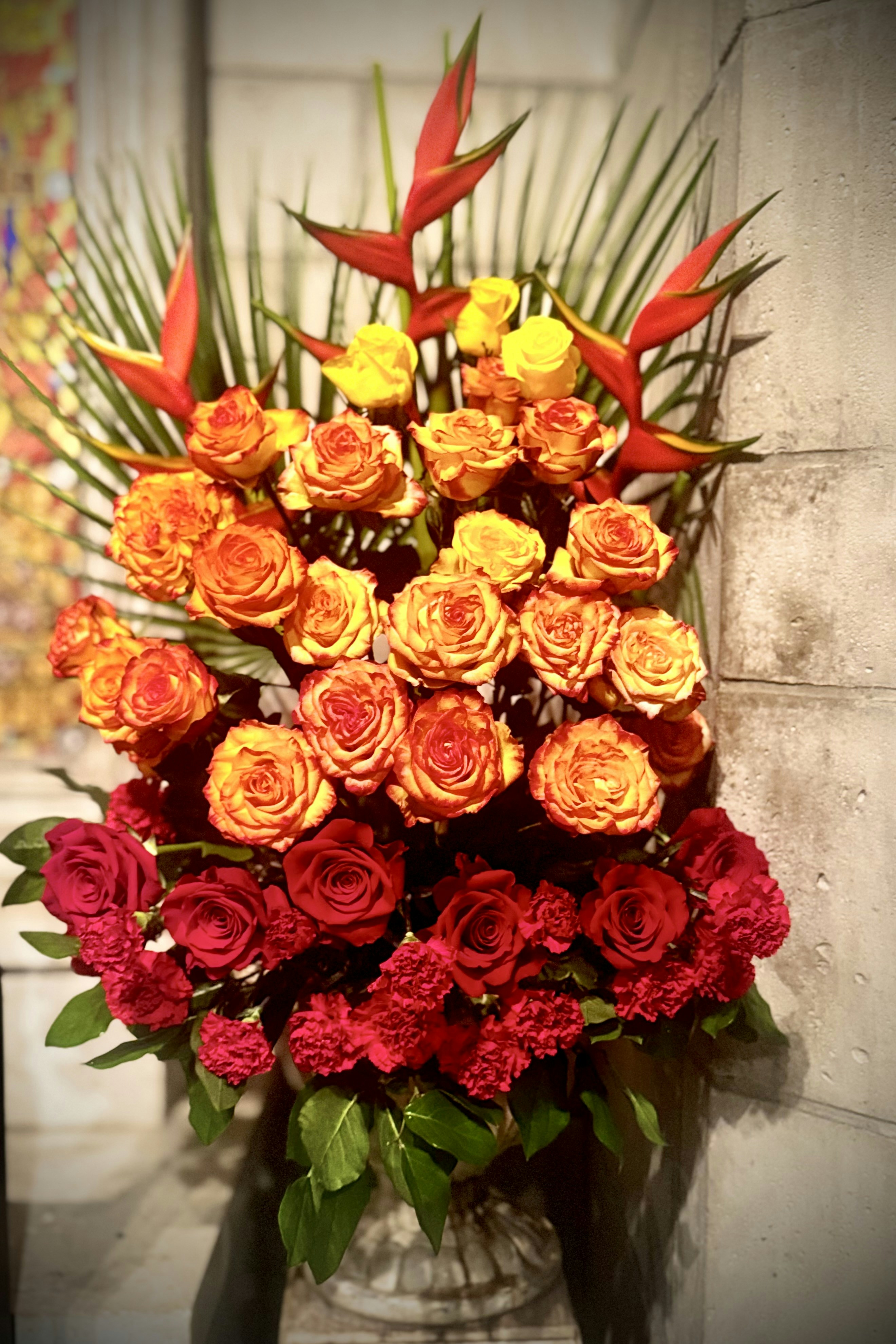 Vivid Bouquet of Orange, Yellow, and Crimson Roses Against a Stone Wall