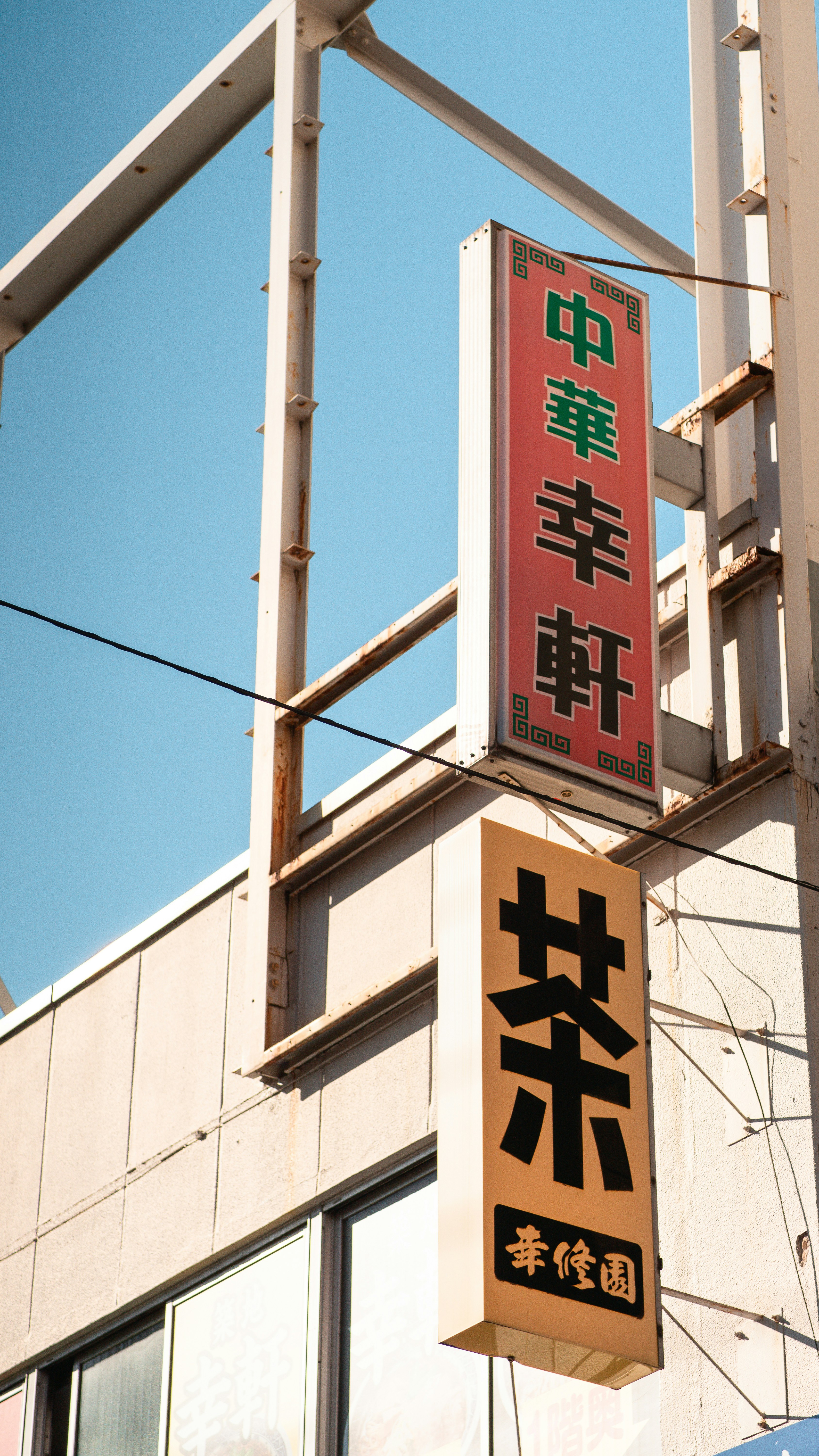 Vertical Lanterns Stand Beside a Sunlit Urban Façade