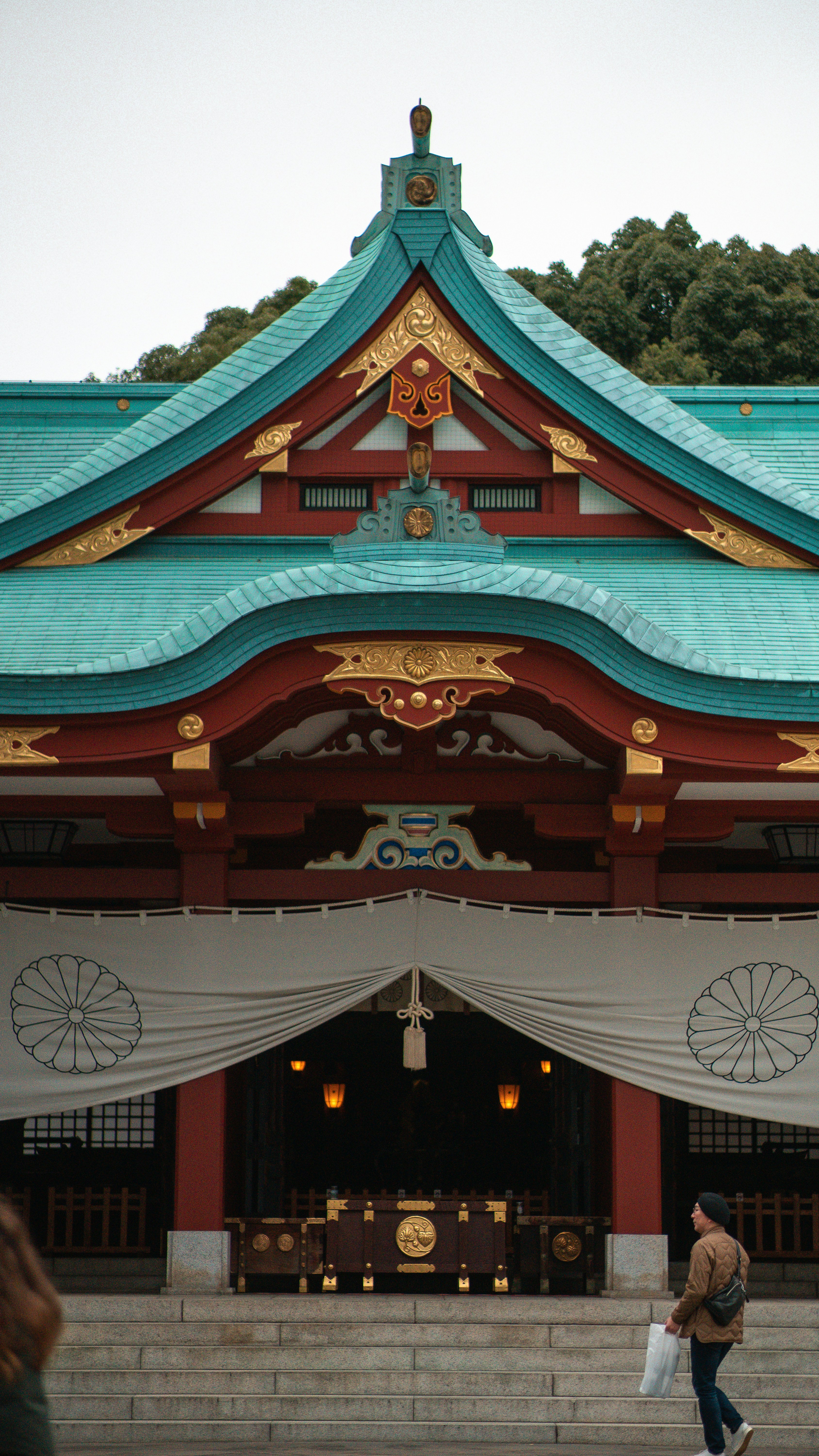 Curved teal roofs and gold ornaments over a Shinto temple entrance