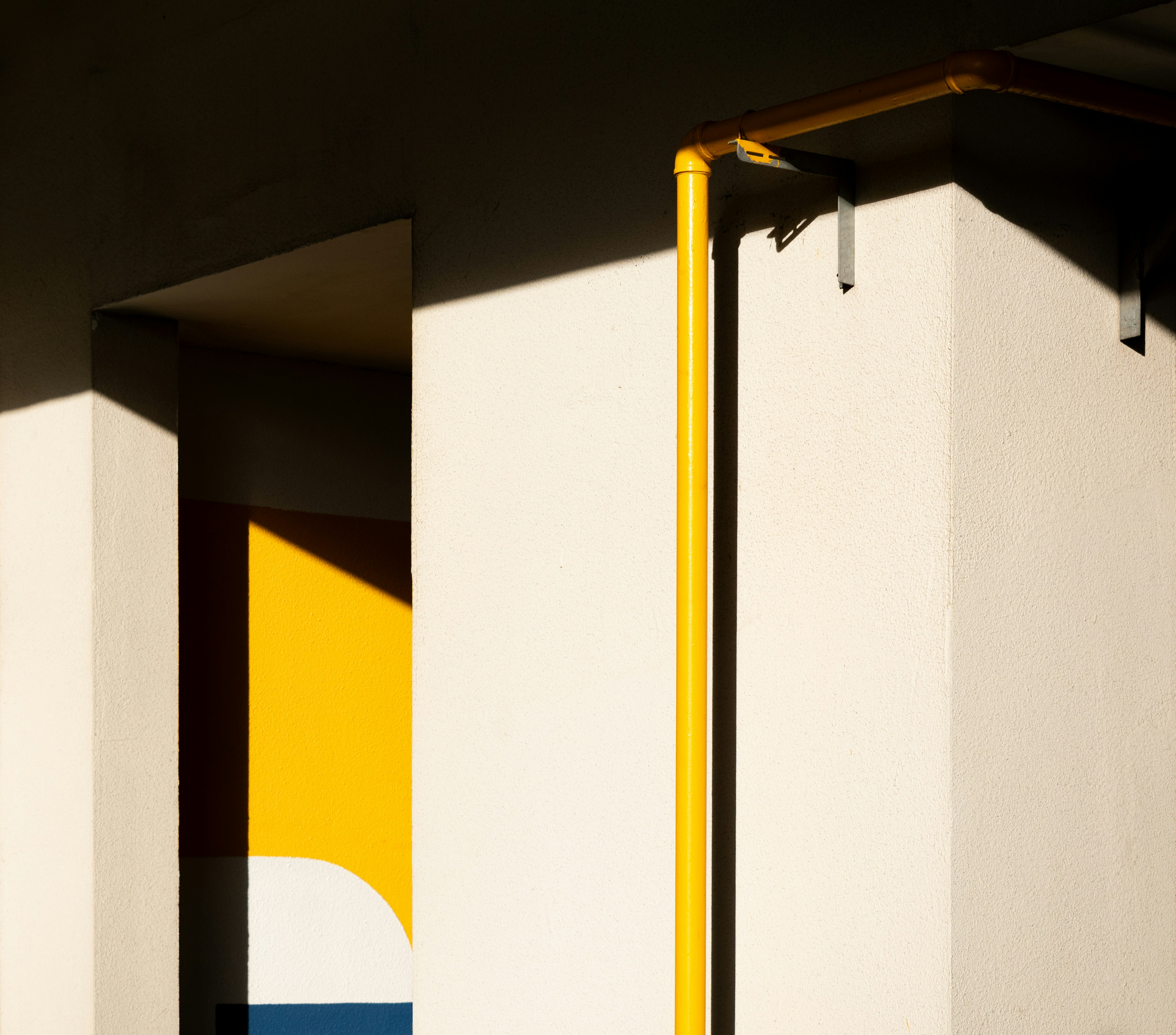 Sunlit Yellow Pipe Framing a Shadowed Architectural Accent