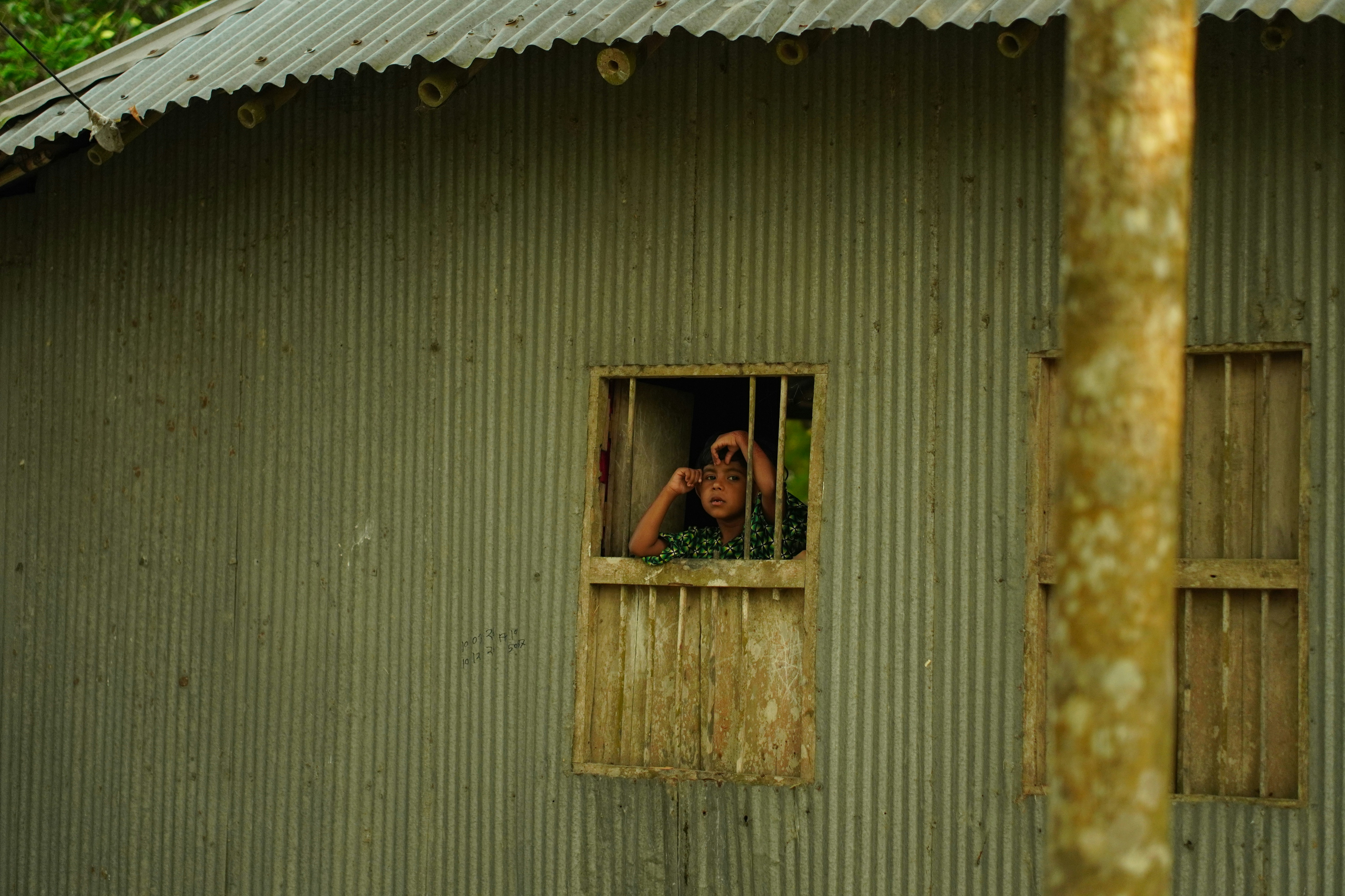 Window of Quiet Focus: A Child at the Corrugated Wall