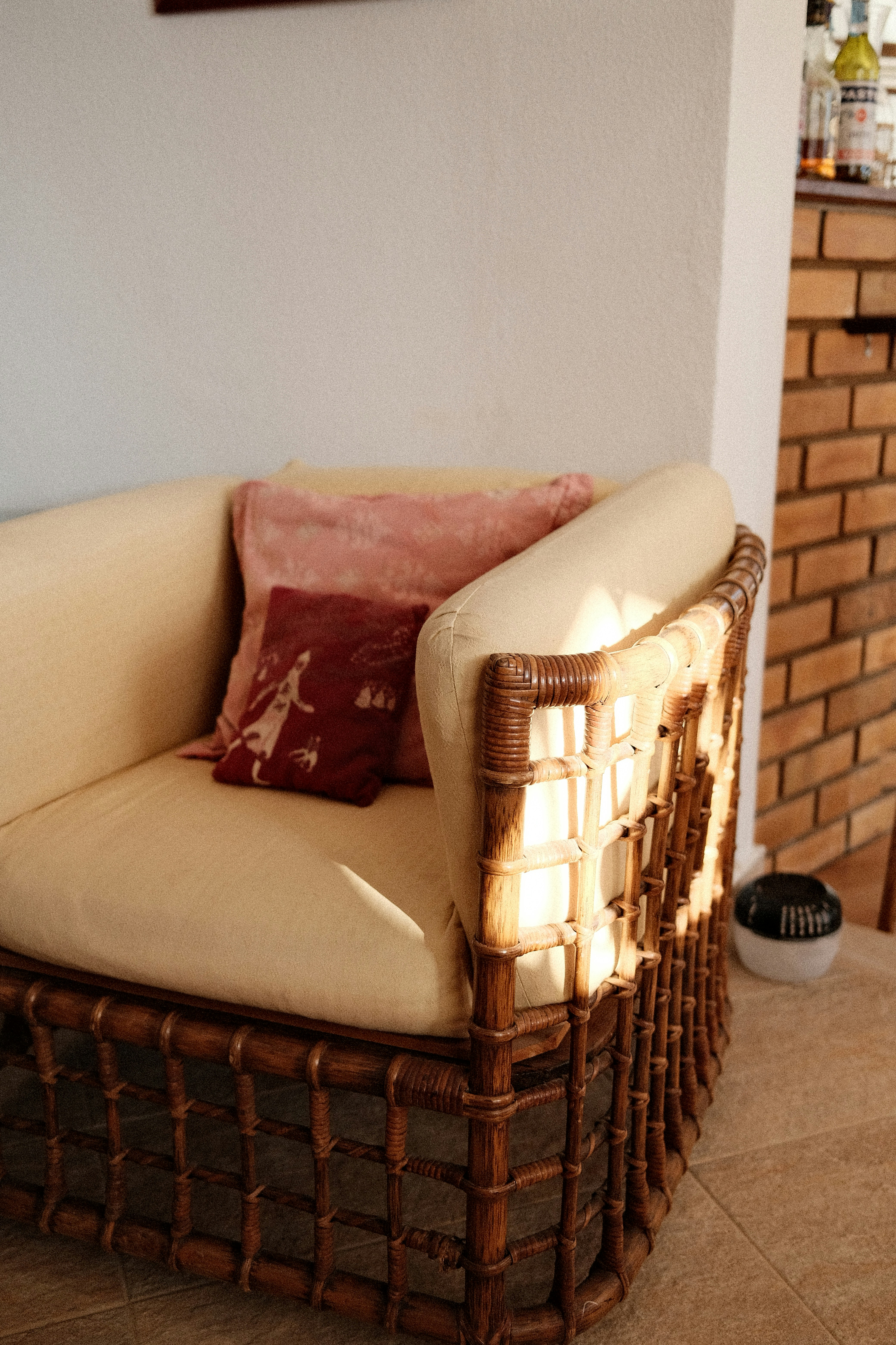 Sunlit Rattan Corner: Cozy Armchair with Cushions by a Brick Nook