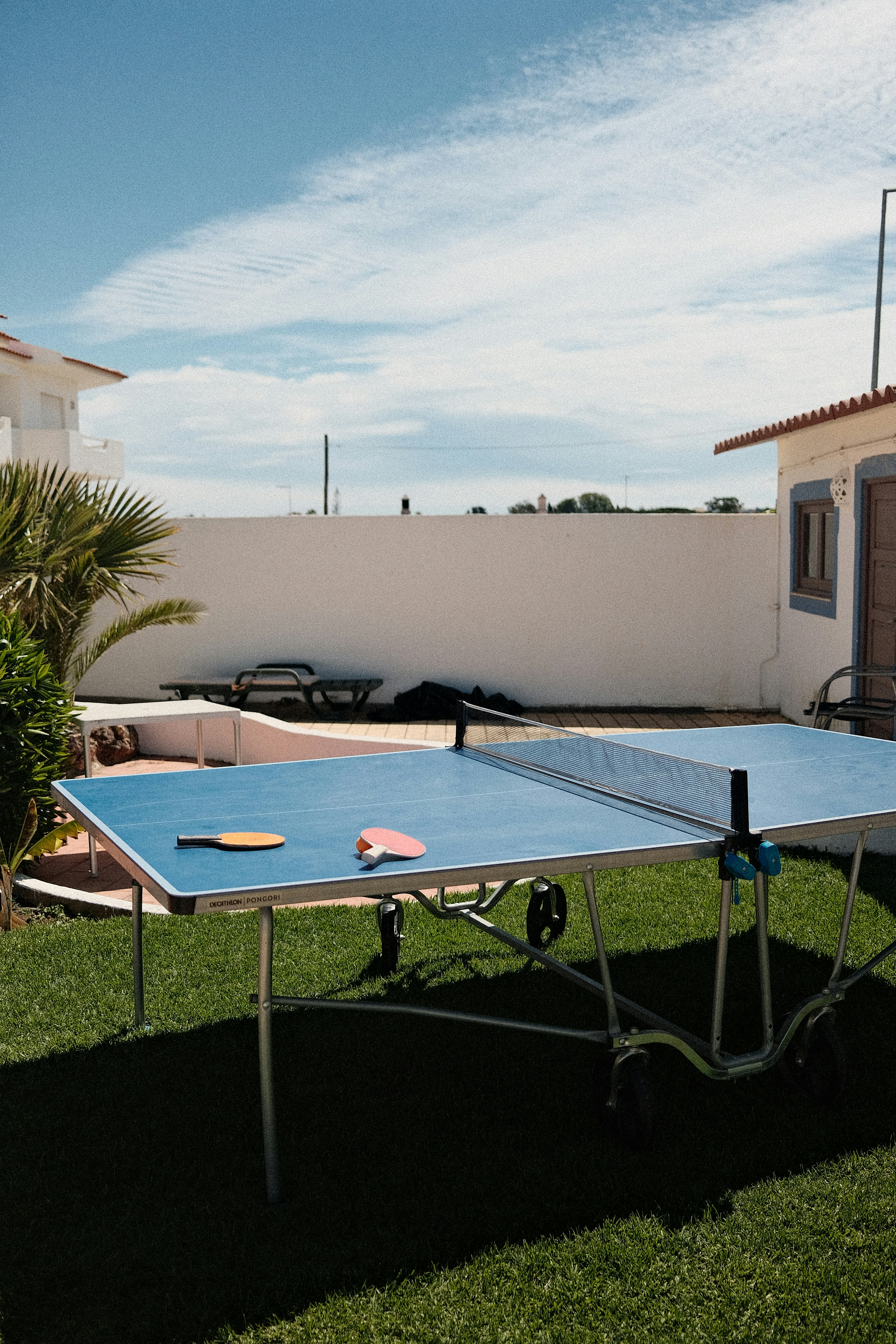 Table tennis in the sunlit backyard: blue paddles resting on a foldable table