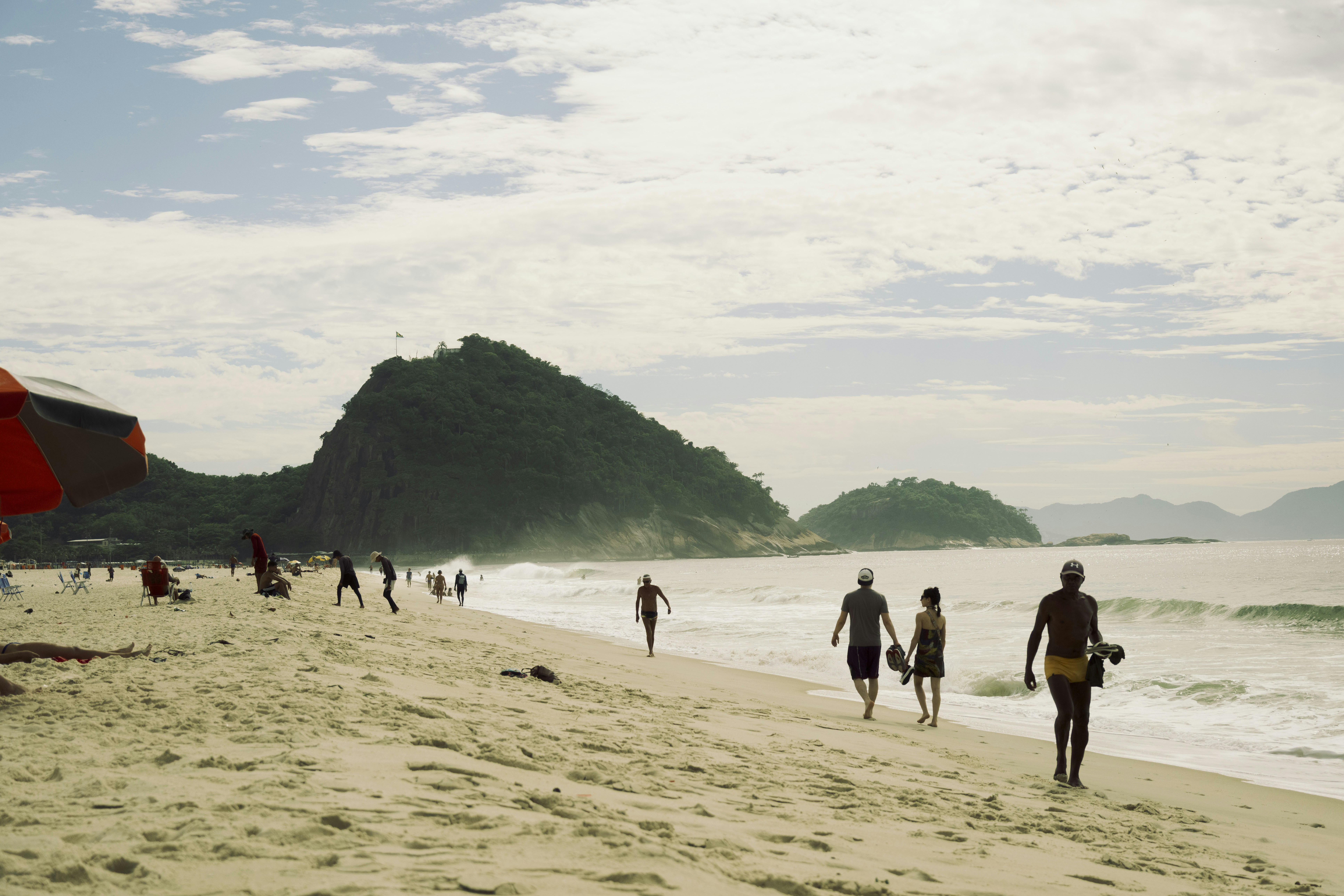 Sunlit Shoreline: People Walk the Wide Beach Toward Emerald Islands