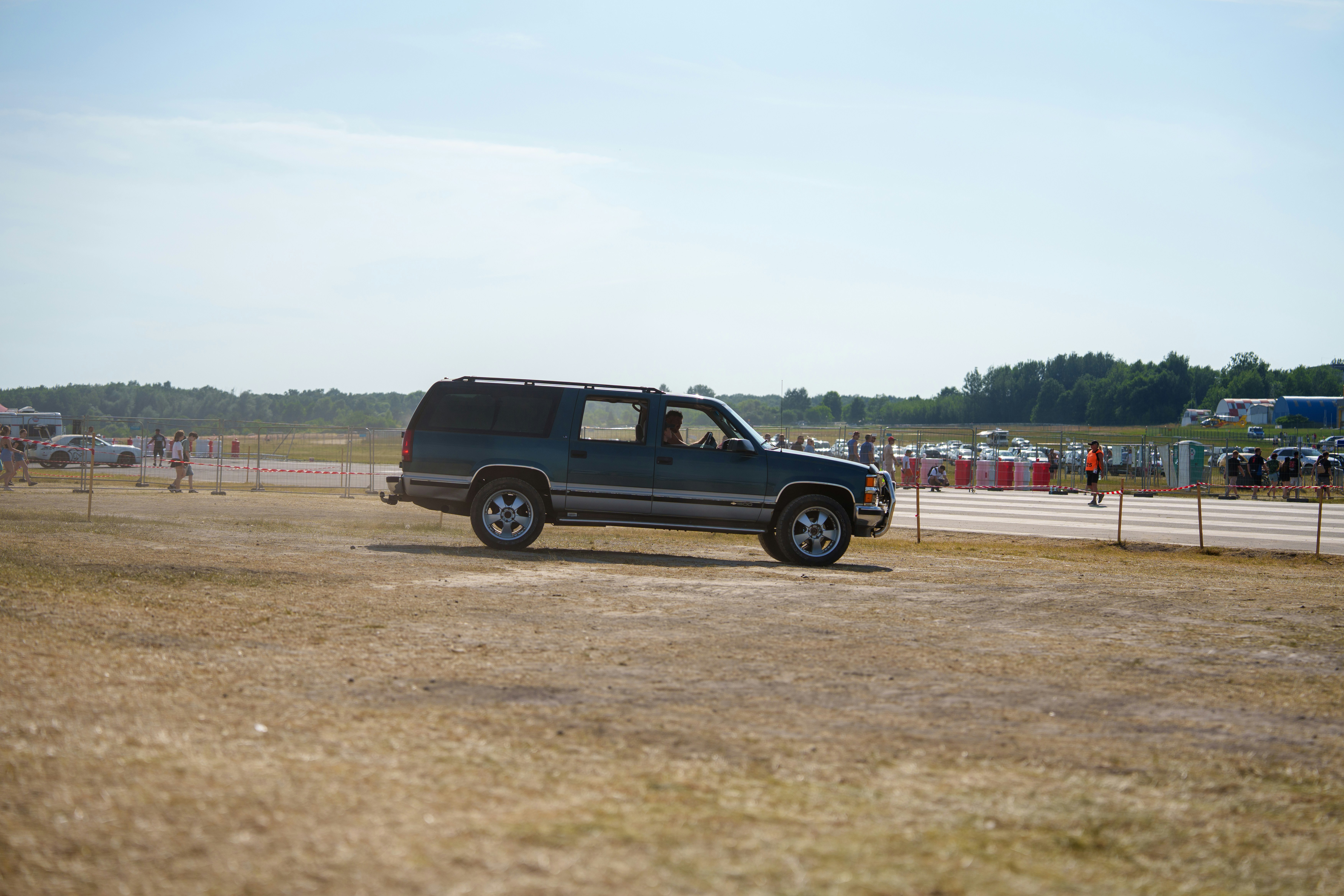 Blue SUV Drives Across a Sunlit Open Field at an Outdoor Event