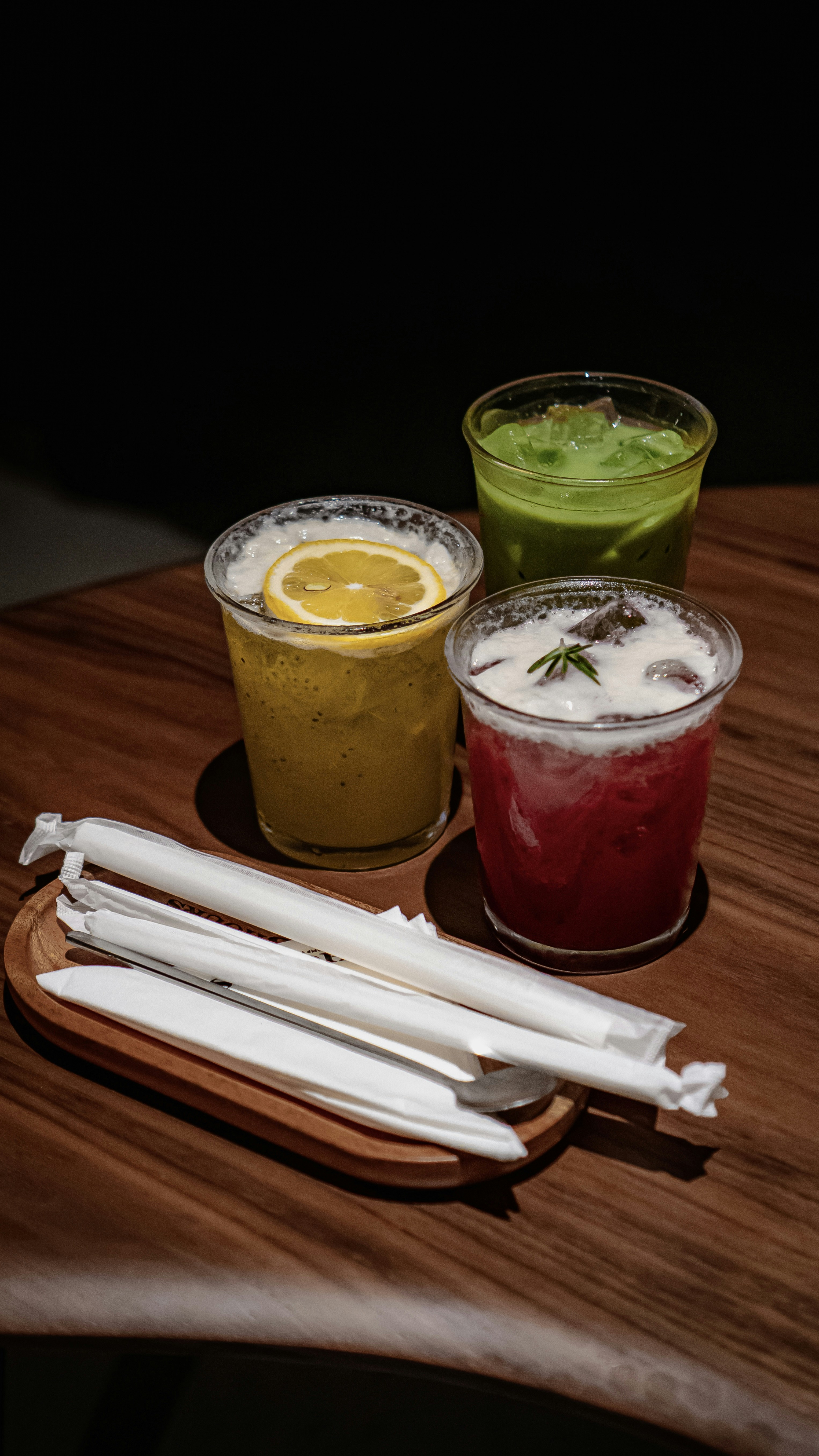 Three vibrant cocktails on a wooden bar with citrus and herb garnishes