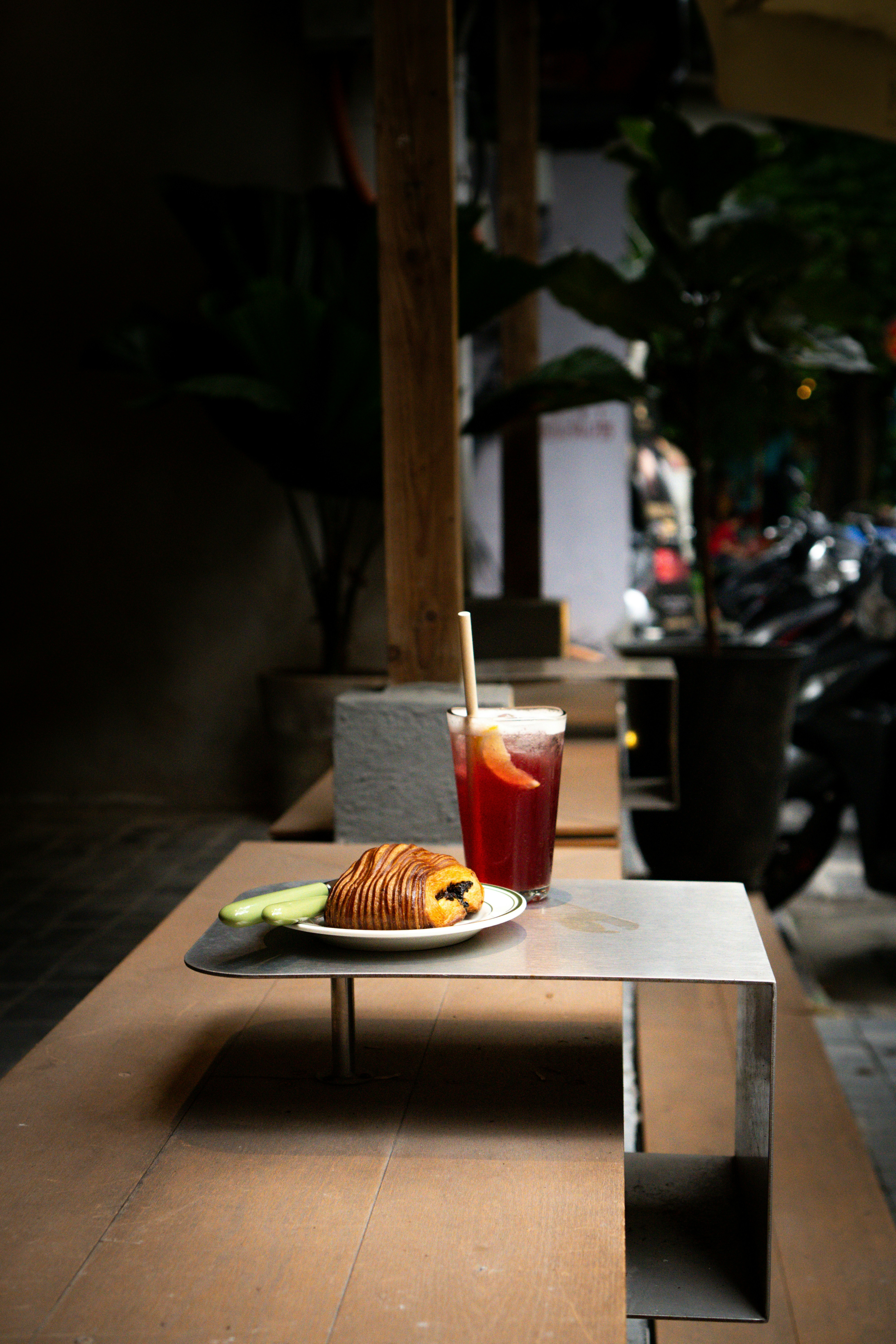 A Quiet Espresso Moment: Pastry, Juice, and Slender Brackets on a Street-side Table
