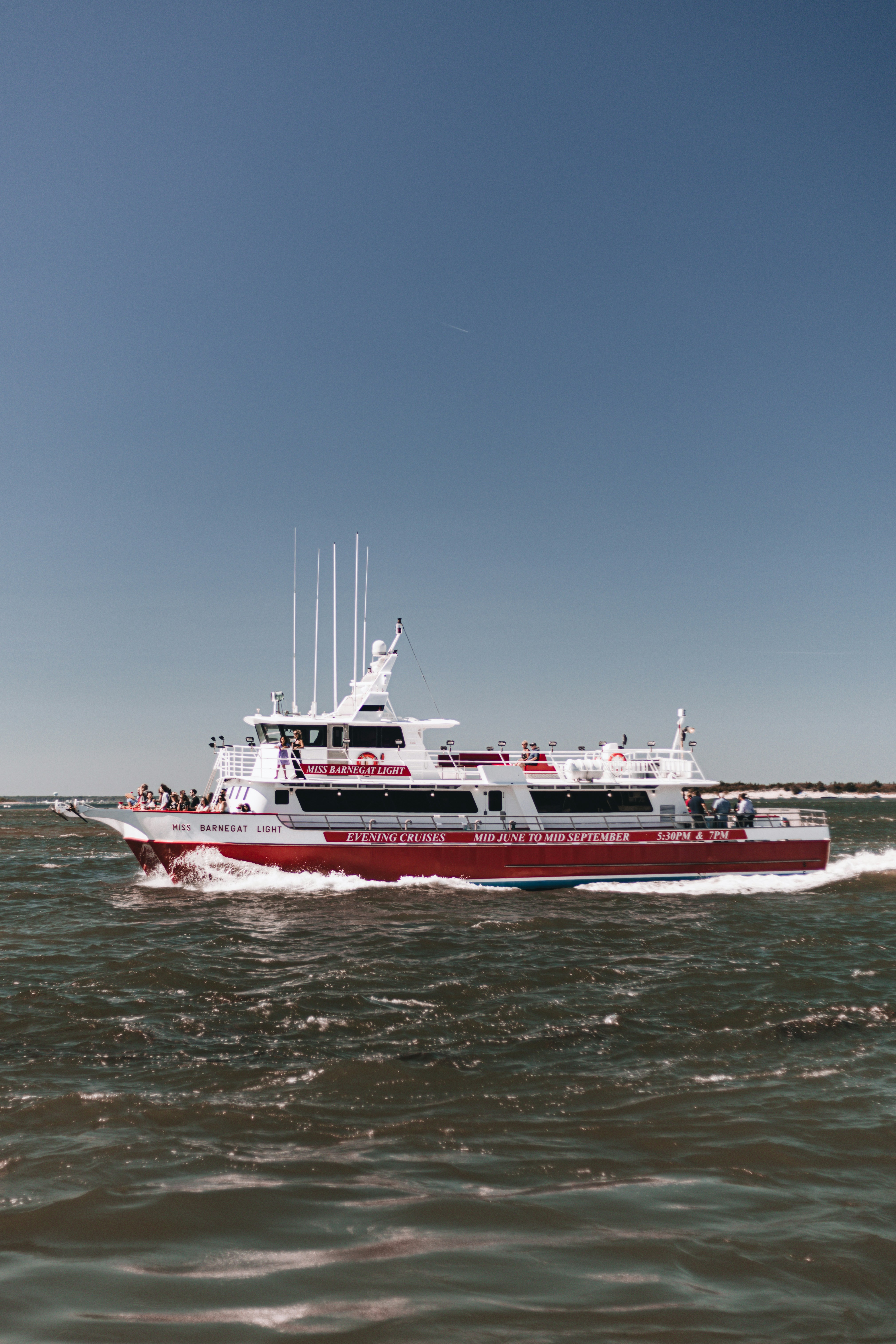 Red and white ferry slicing through choppy waters under a clear midday sky