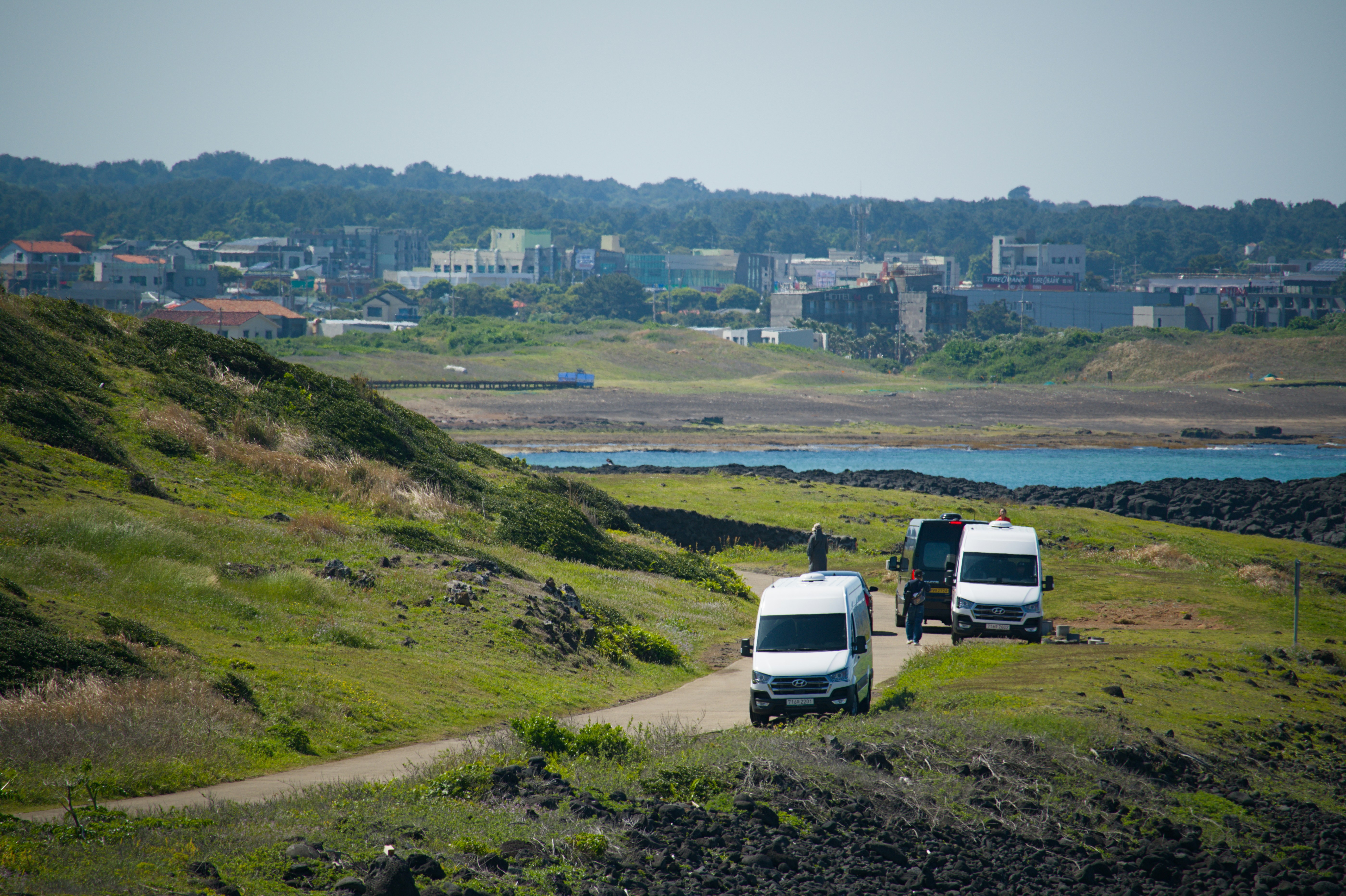 Two Delivery Vans Climb a Coastal Path Toward the City