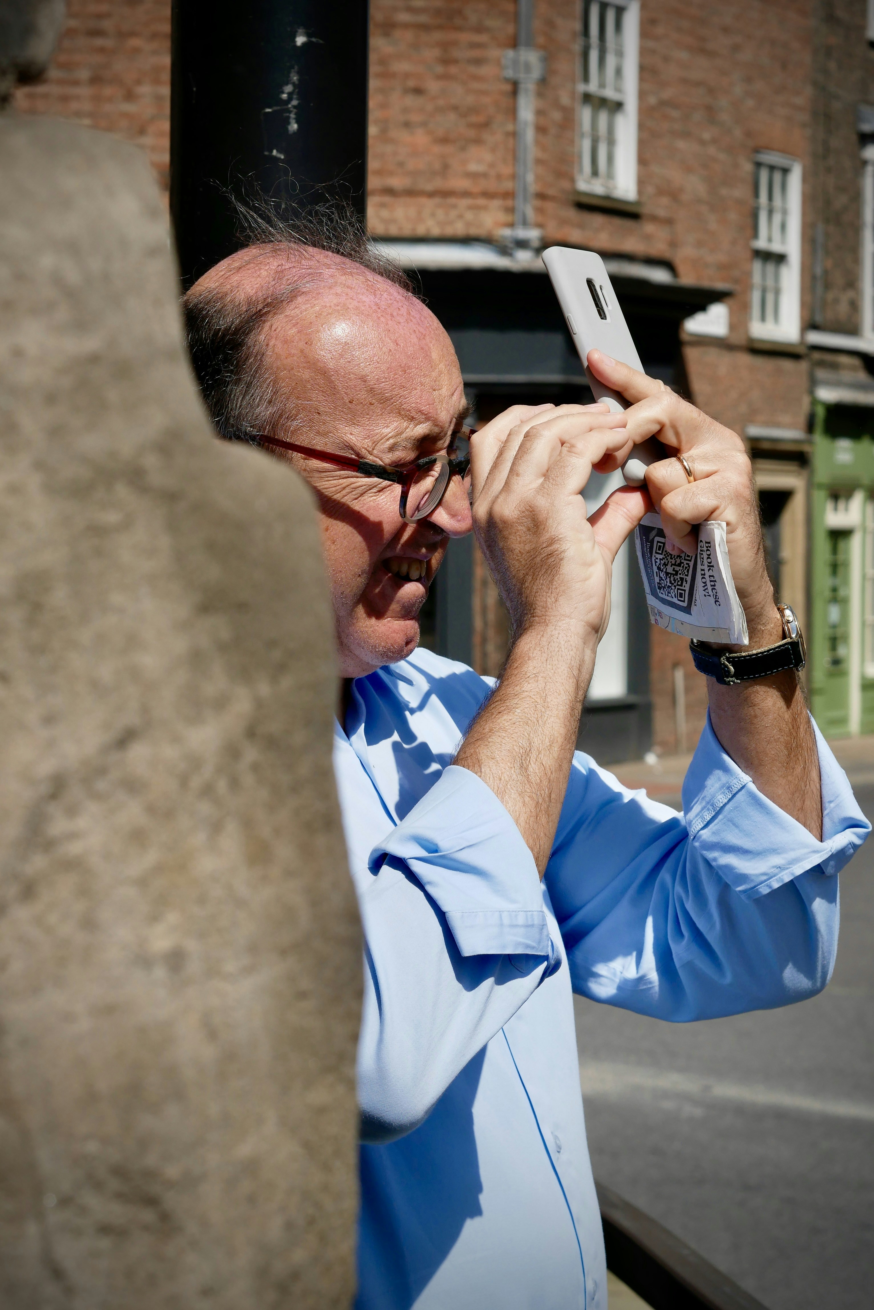 A Moment Captured: Man Adjusts a Smartphone in Sunlit Street