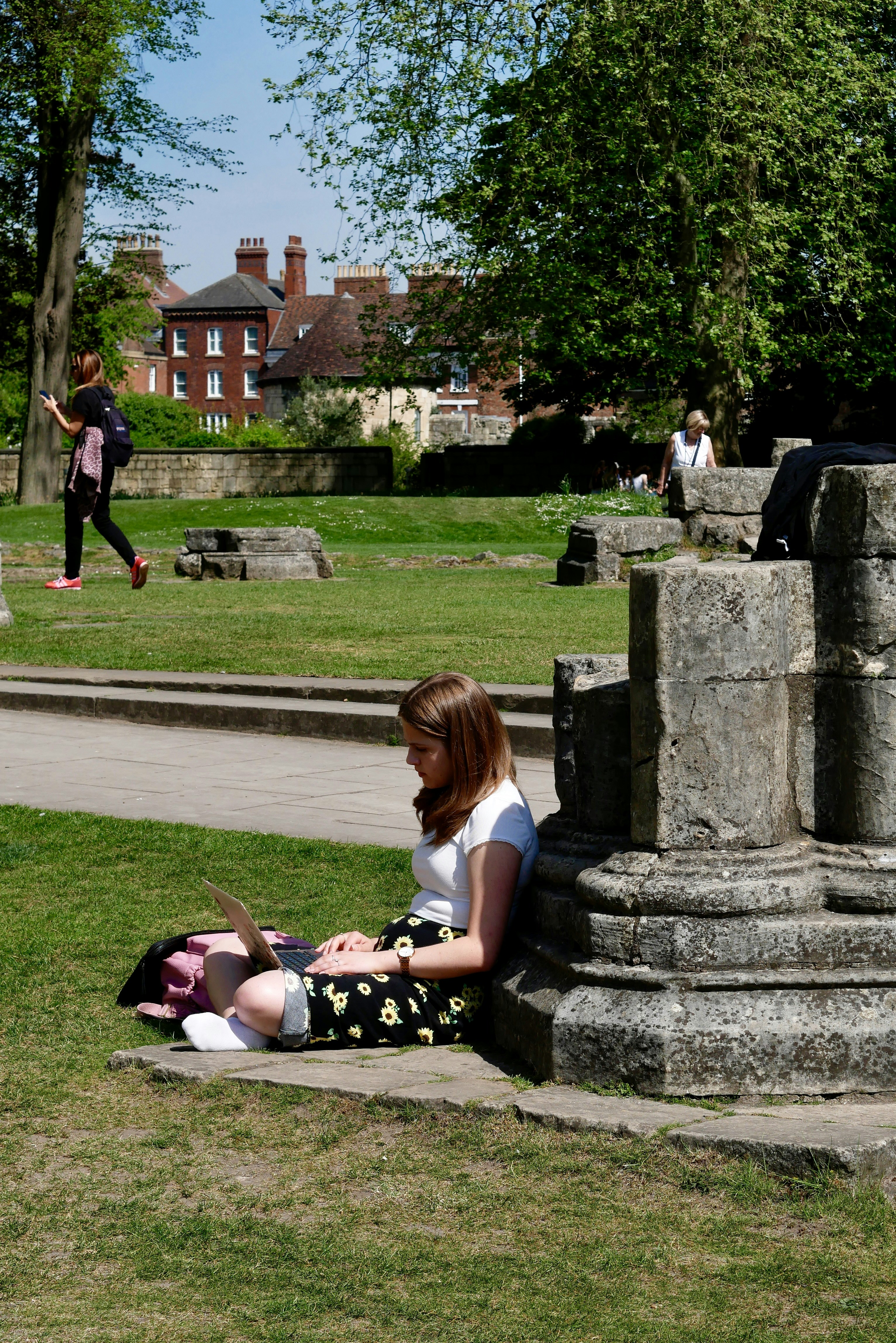 Student in a sunlit park reading beside ancient stonework