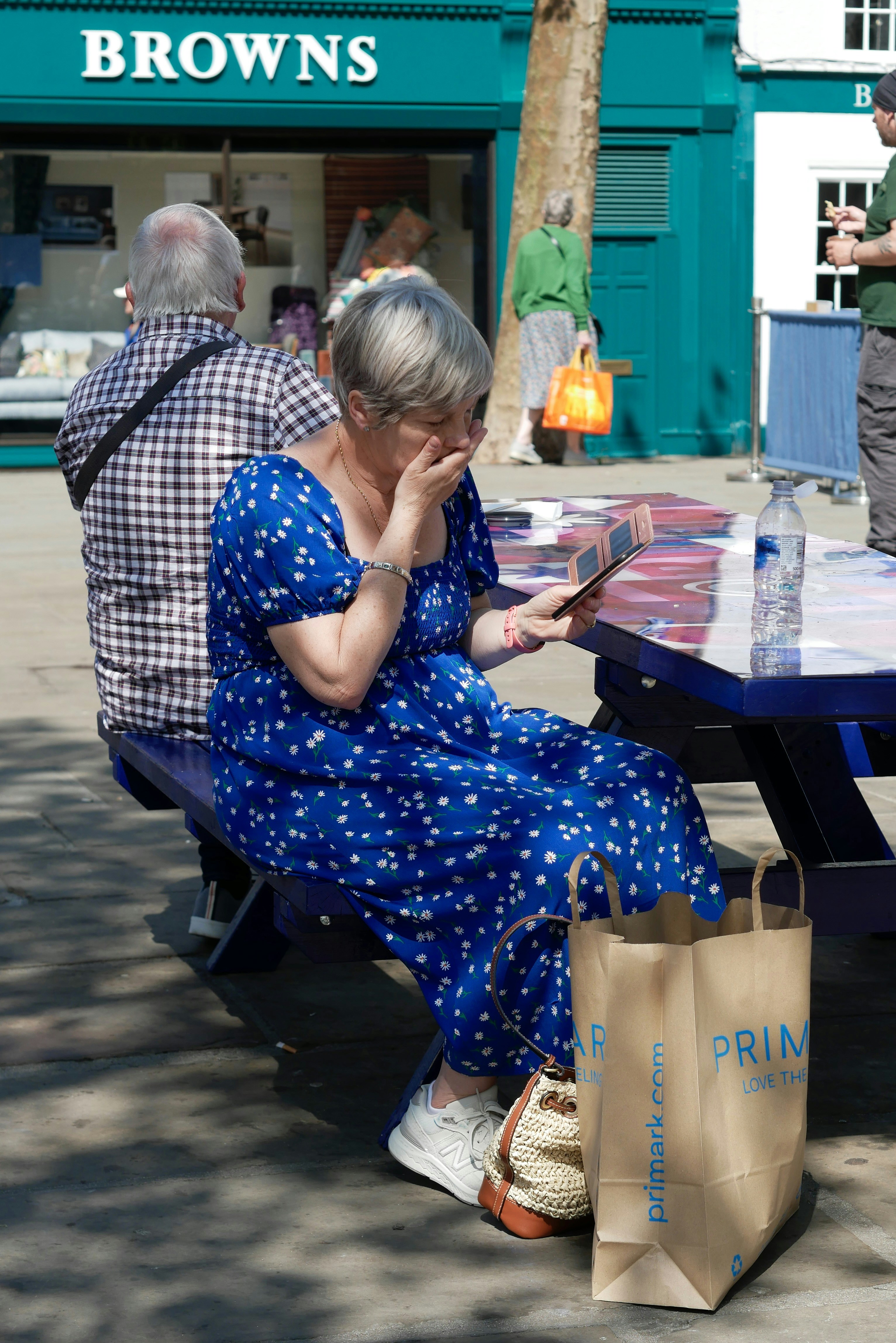 Blue-dotted dress, silent moment: a woman at a sunny street café