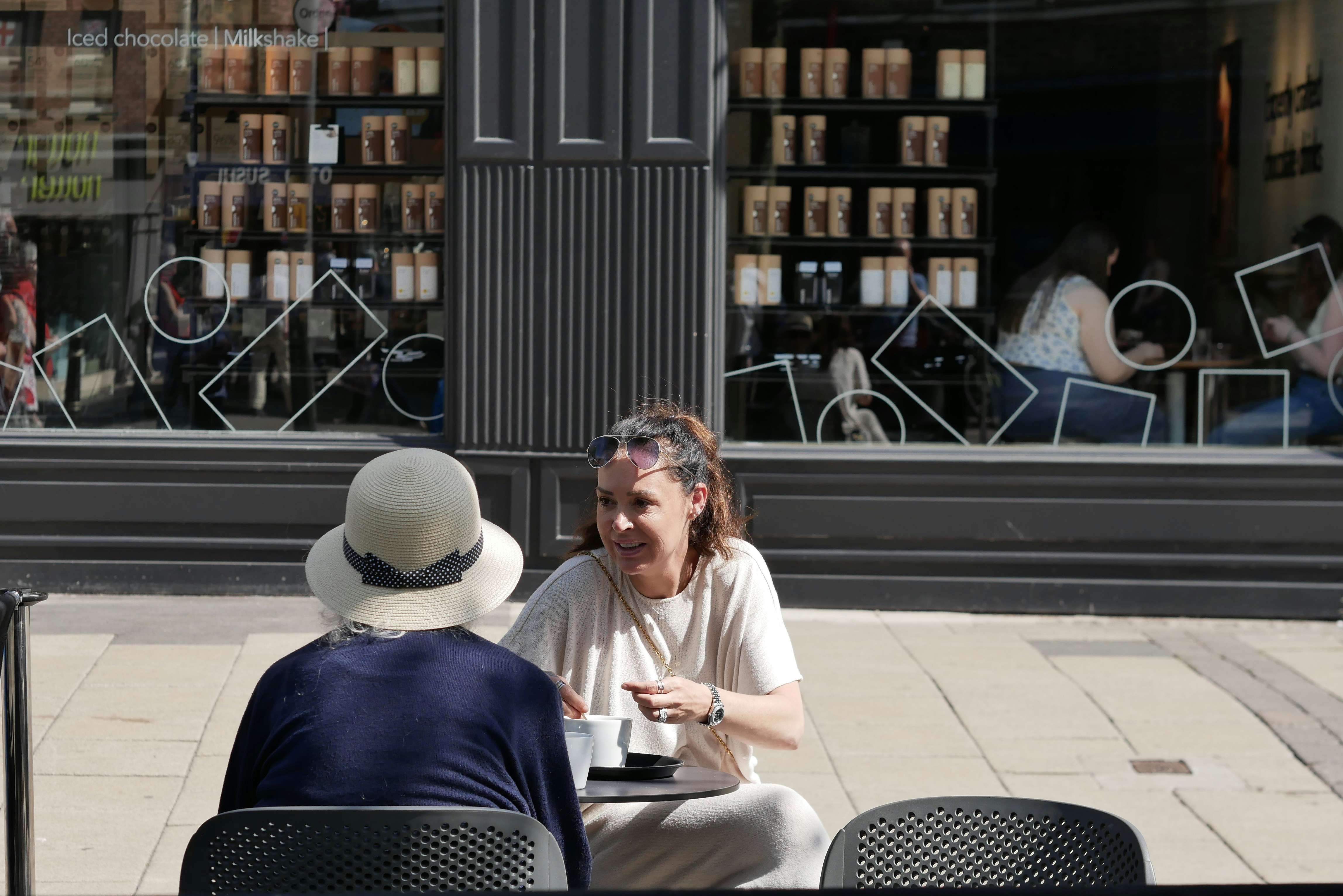 Cafe Conversation Under Glass: Two Women in Quiet Dialogue