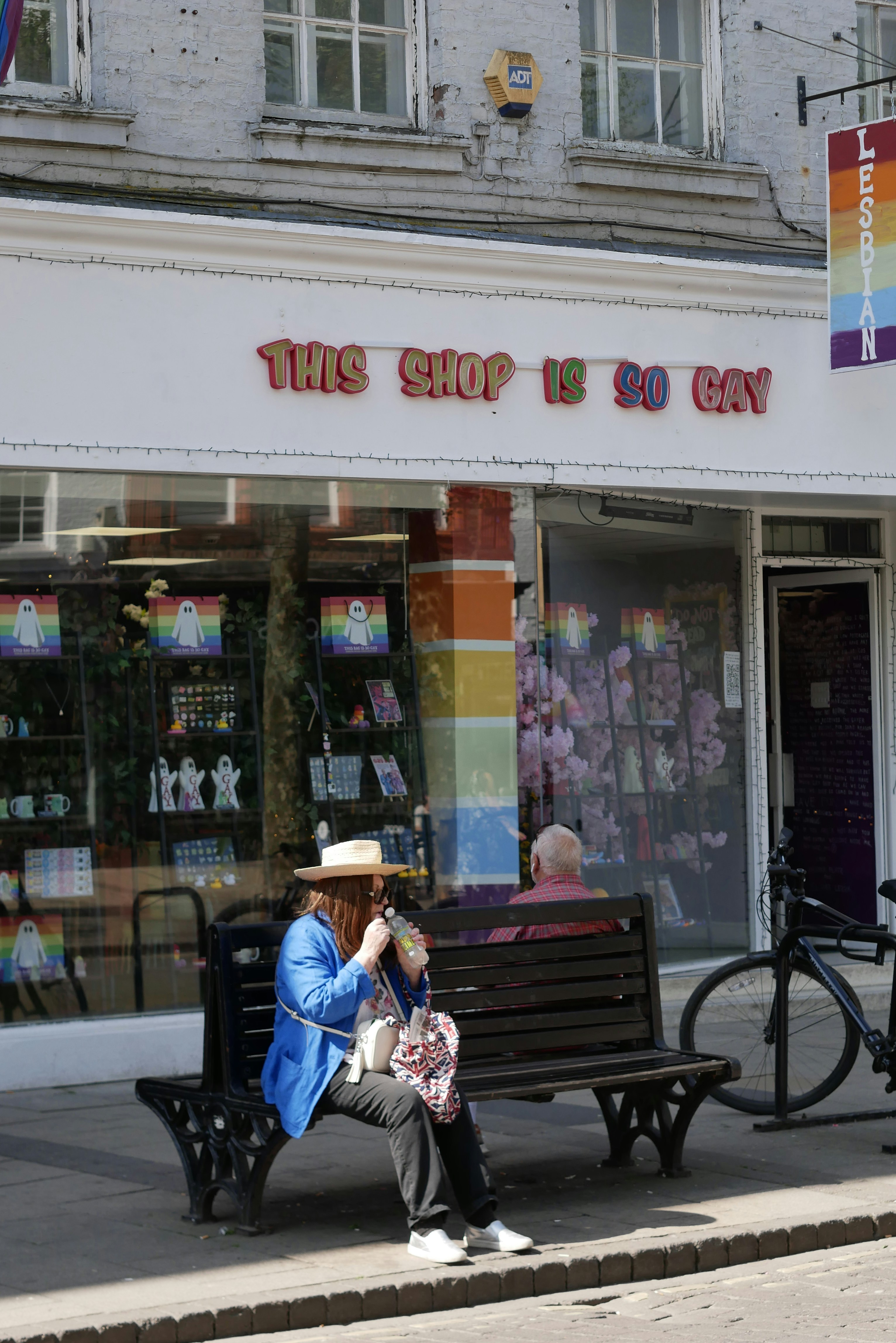 Striking storefront dialogue: a rainbow-pillar shopfront framed by a lone reader on the bench