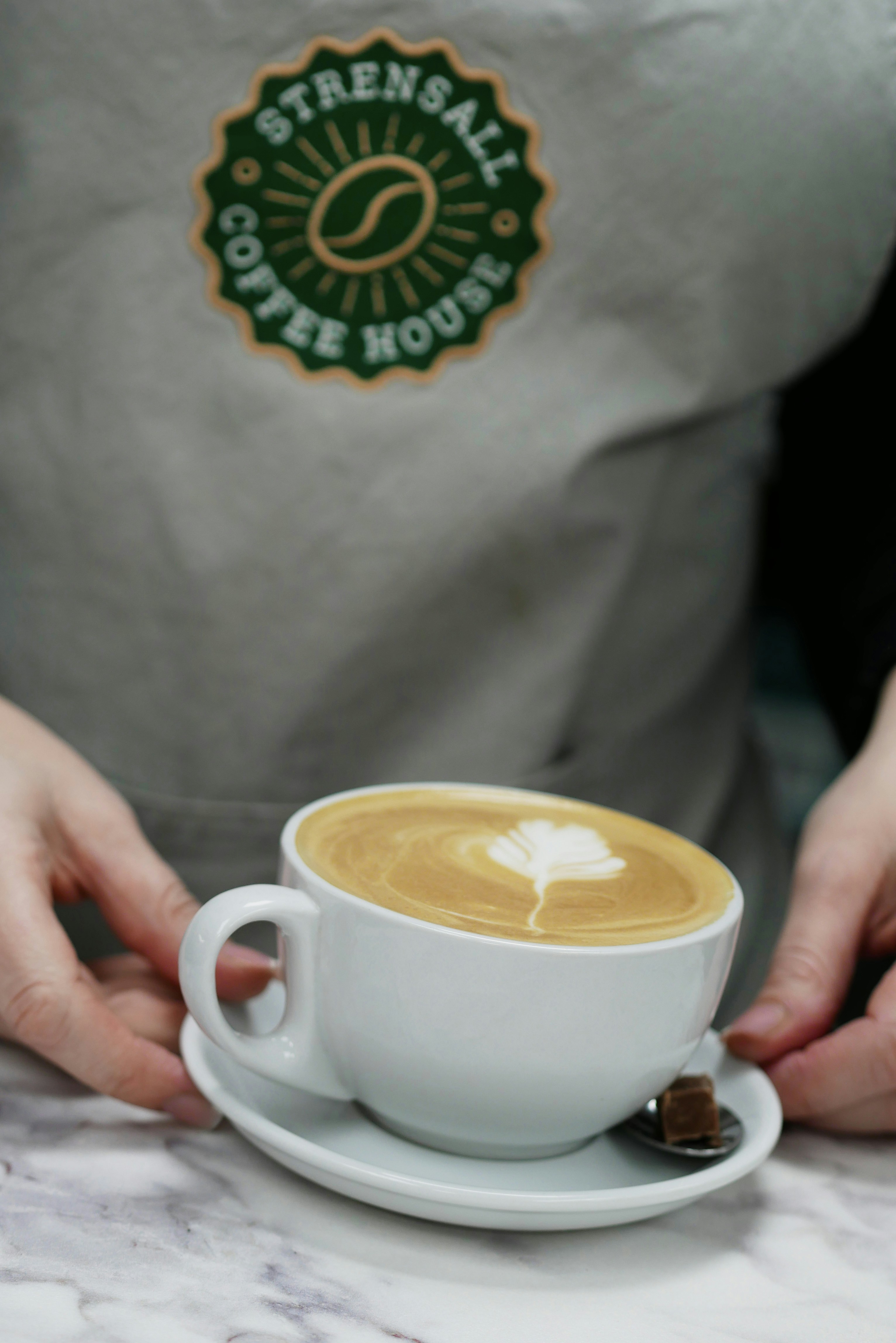 Barista's Craft: Latte Art Framed by a Soft-Focus Shirt Emblem