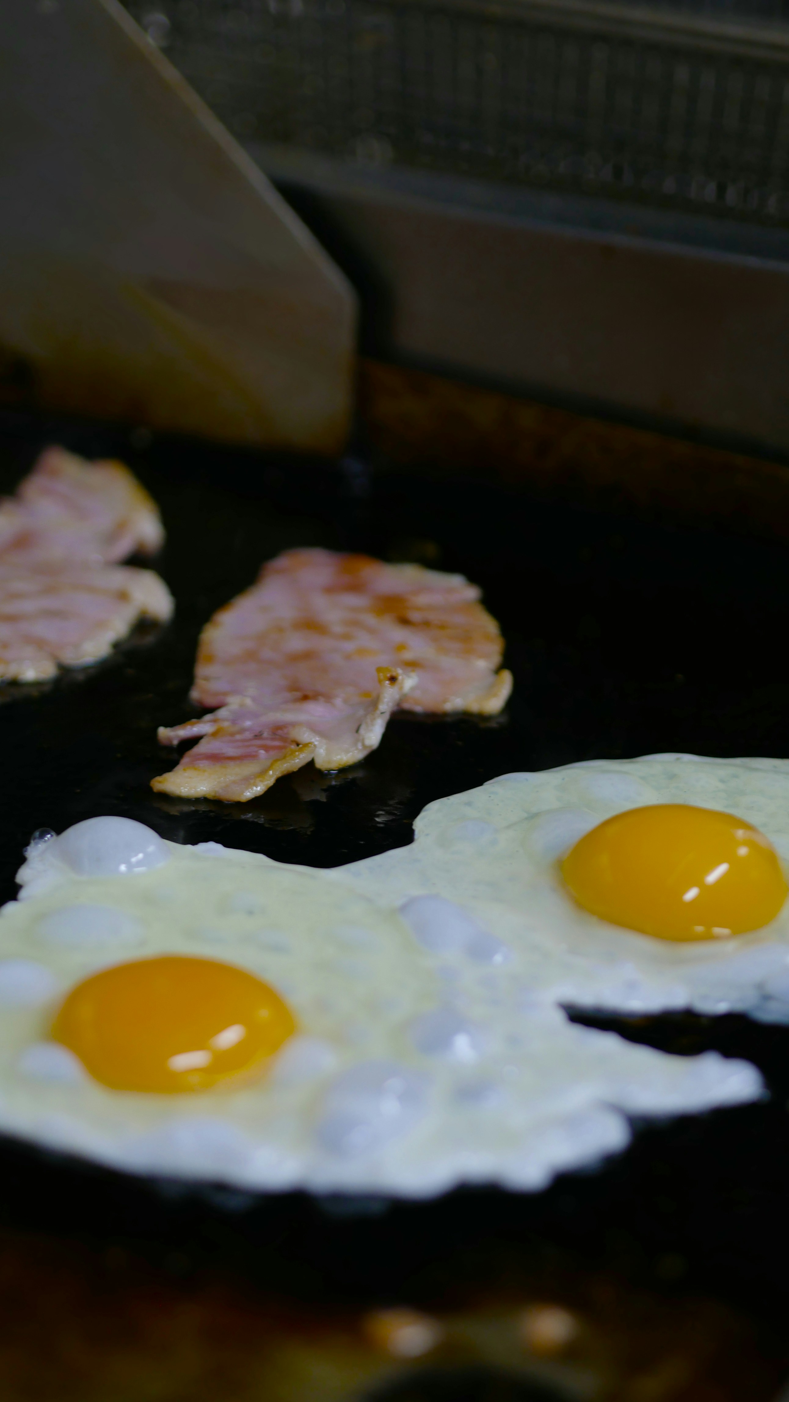 Sunny-side Focus: Eggs Sizzle on a Griddle with Crispy Bacon