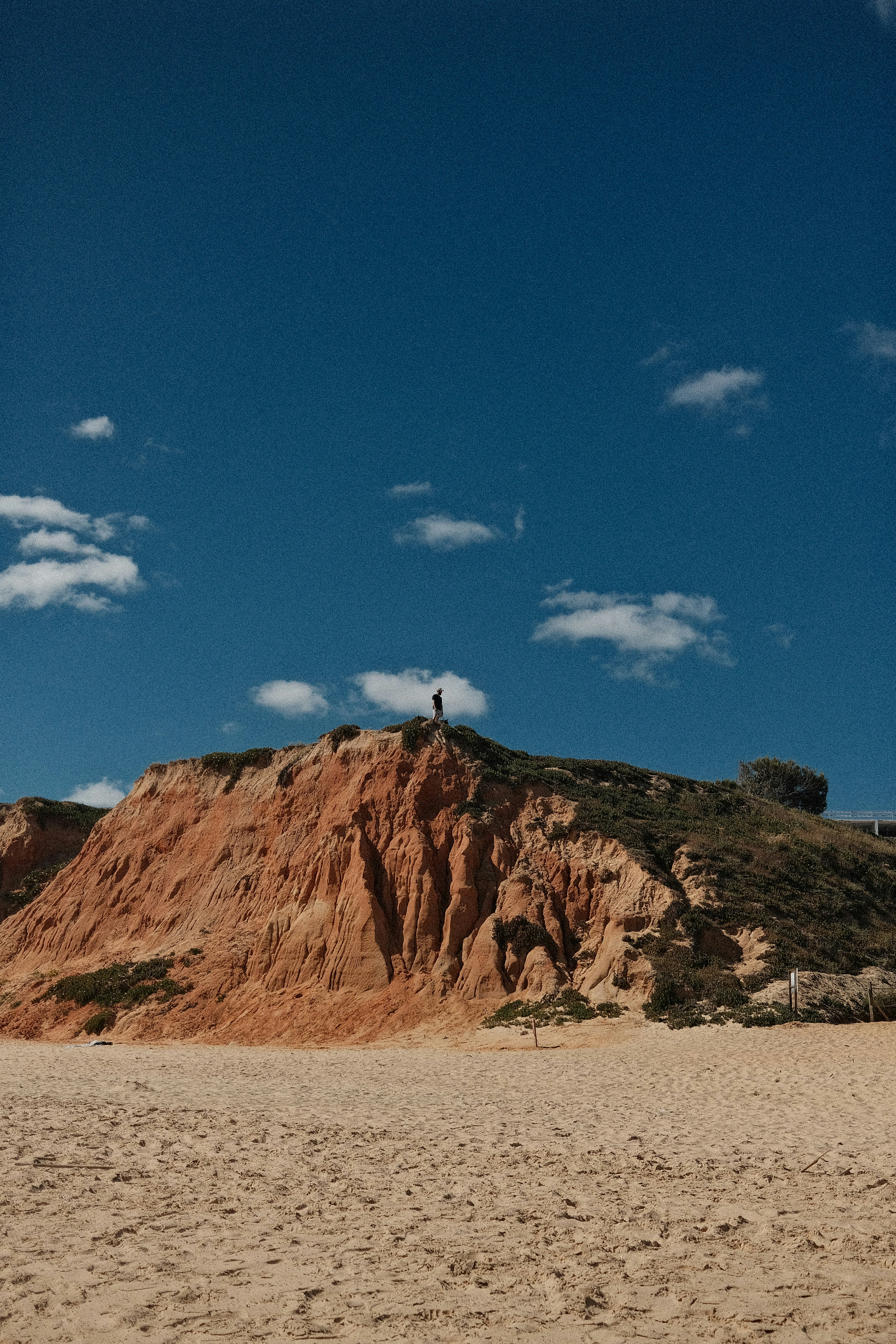 Clifftop Sentinel: A Lone Figure atop Coastal Red Cliffs