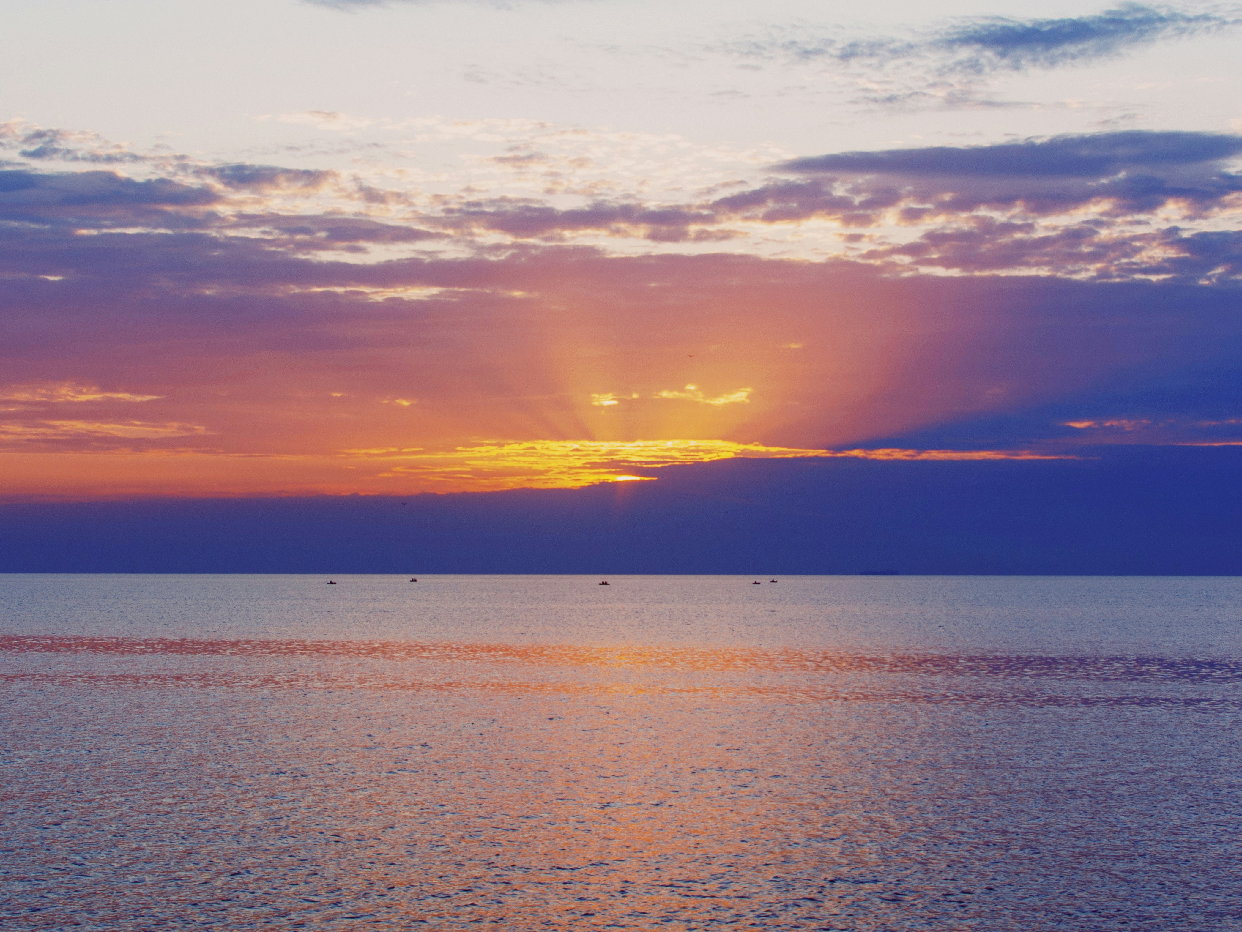 Sunrise Over a Calm Horizon: Rays Break Through Clouds