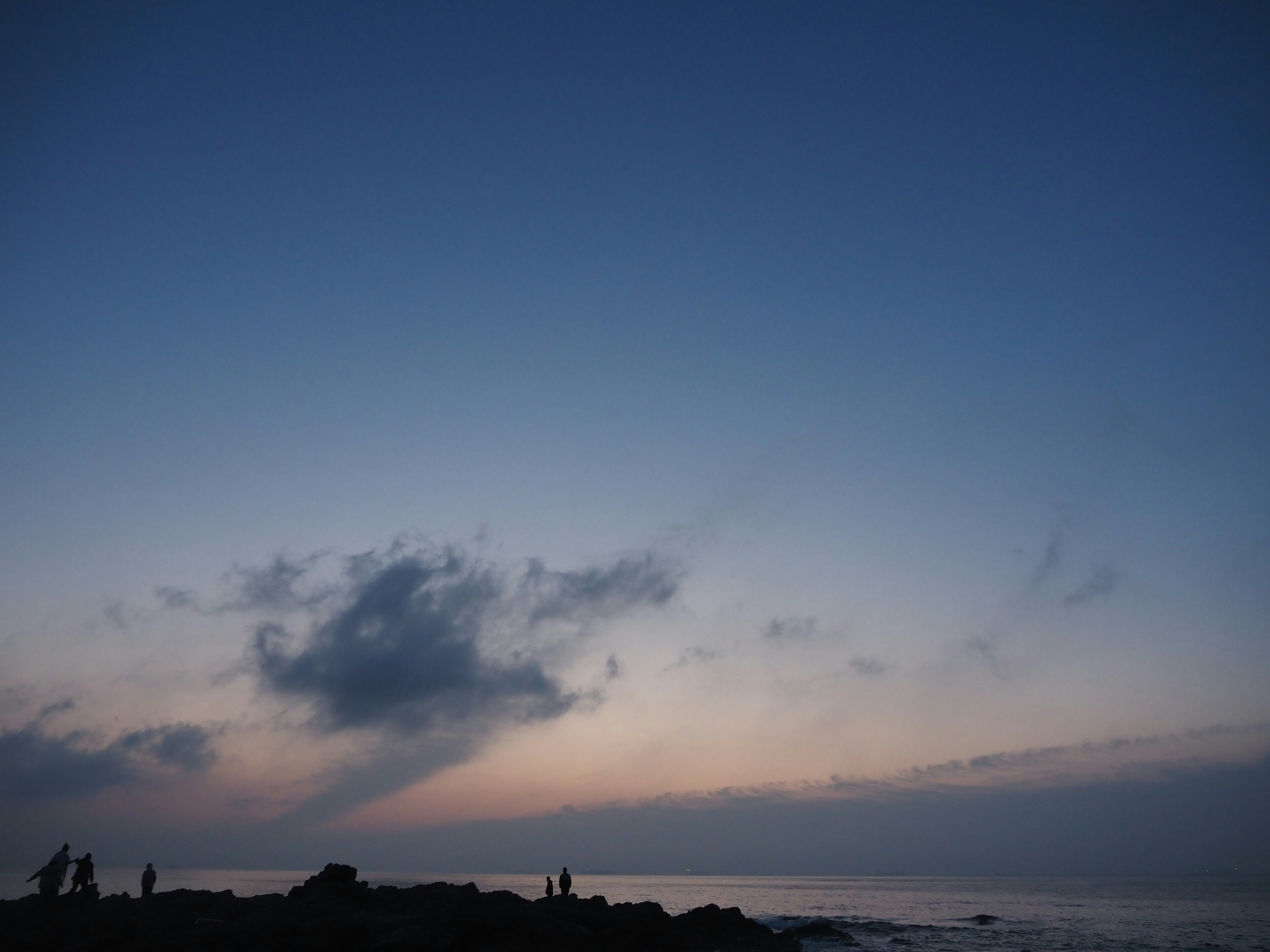 People silhouetted on a rocky shore at dusk.