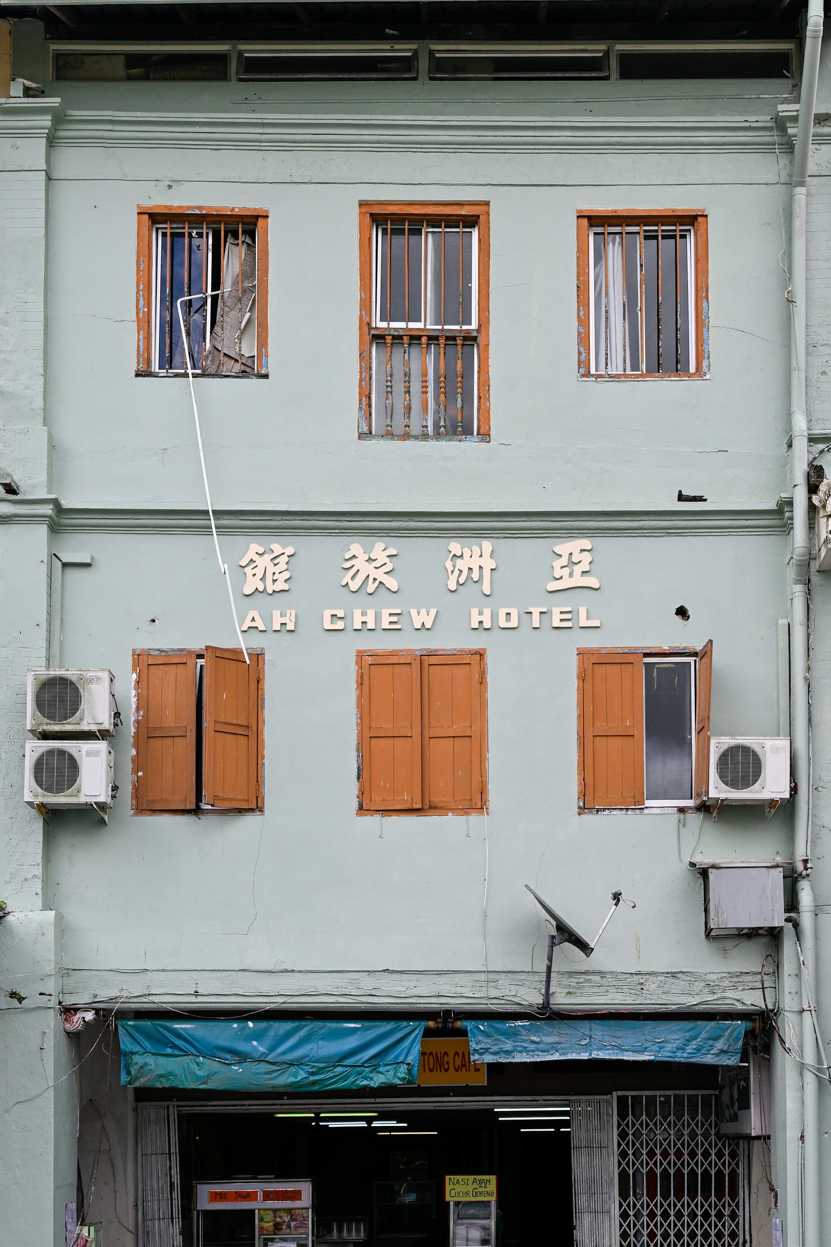 The facade of AH CHEW Hotel: chipped paint, weathered shutters, and a blue awning