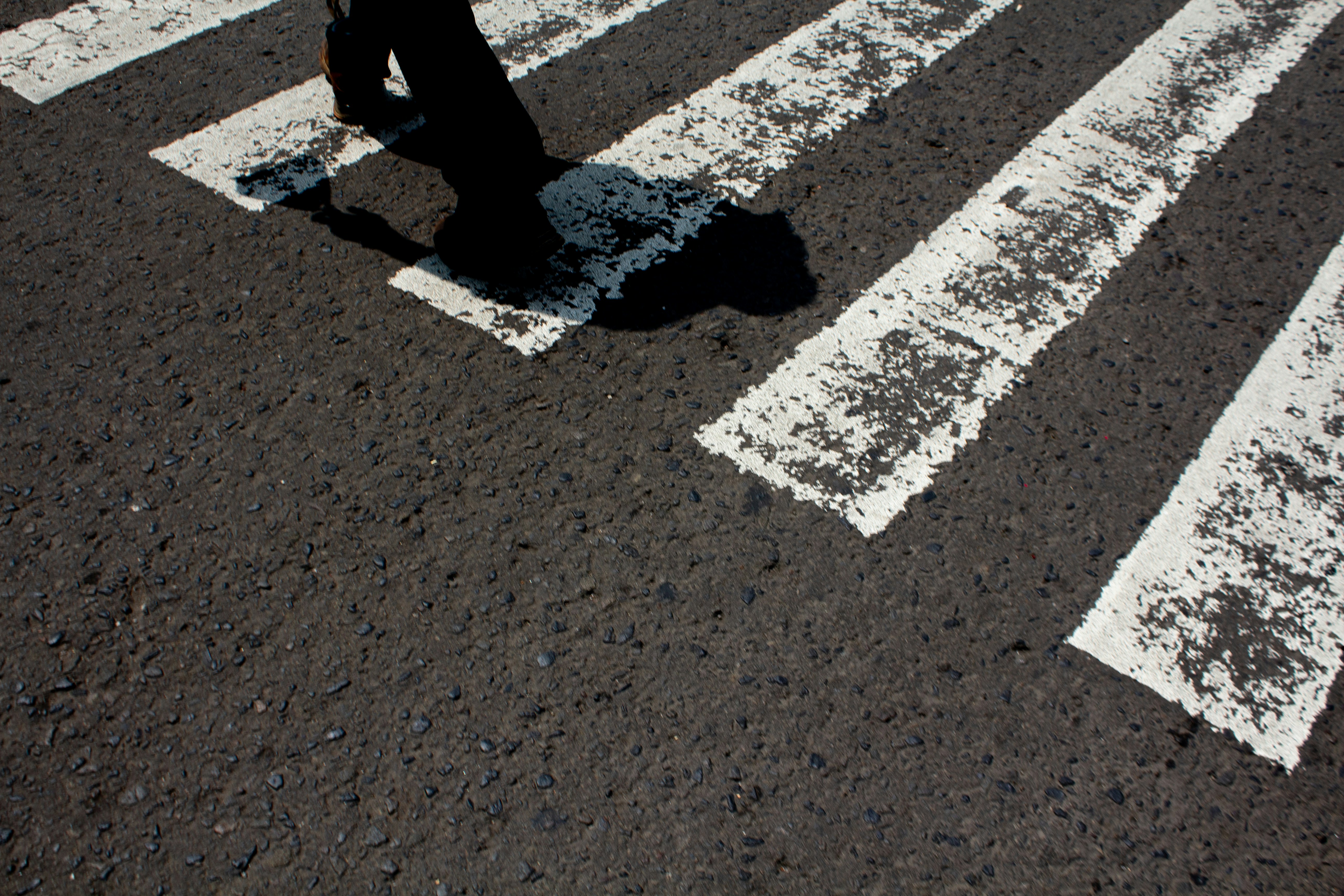 Shadowed Stride Across Weathered Crosswalk