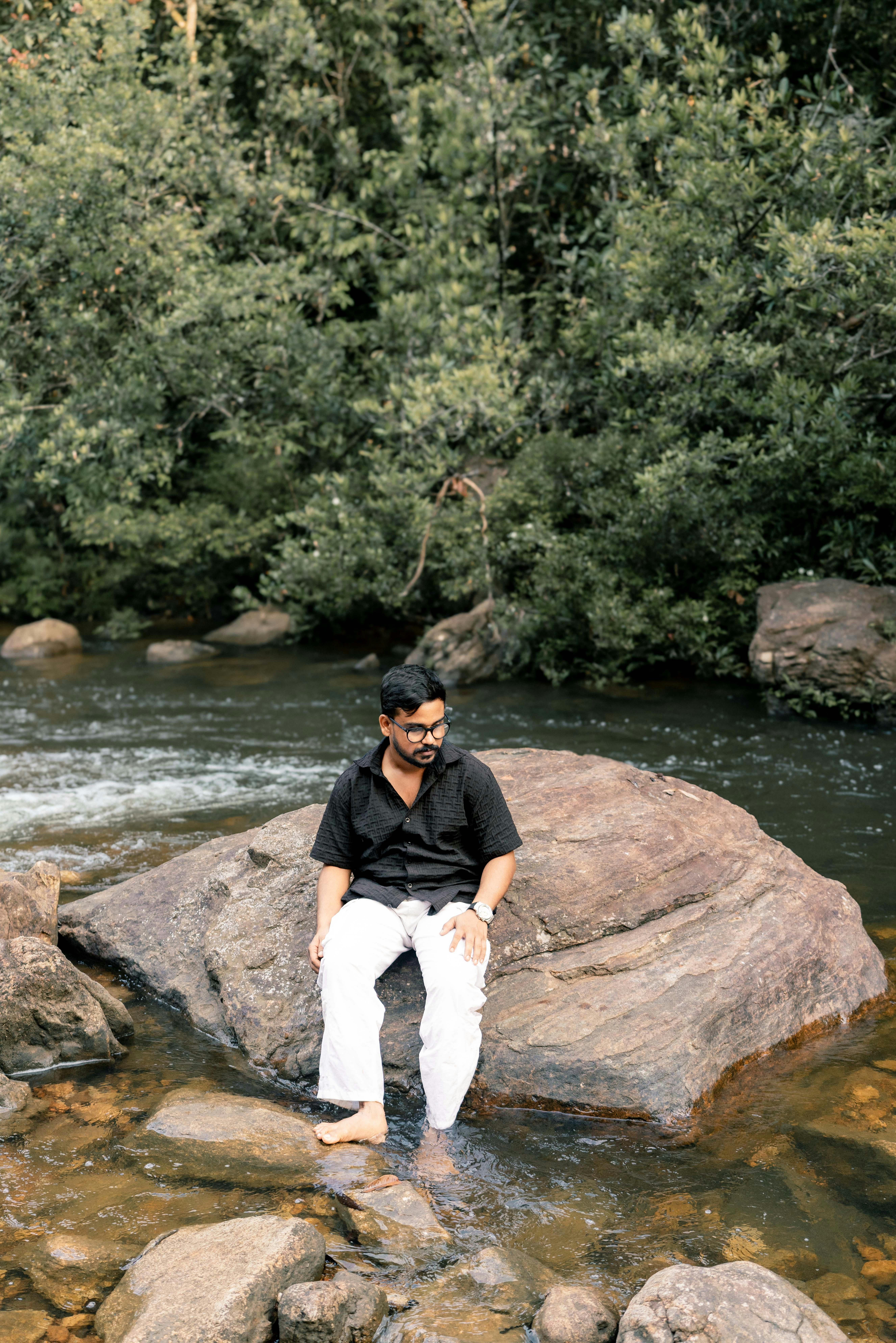 Rugged calm: a man resting on a sun-warmed rock by a forest river