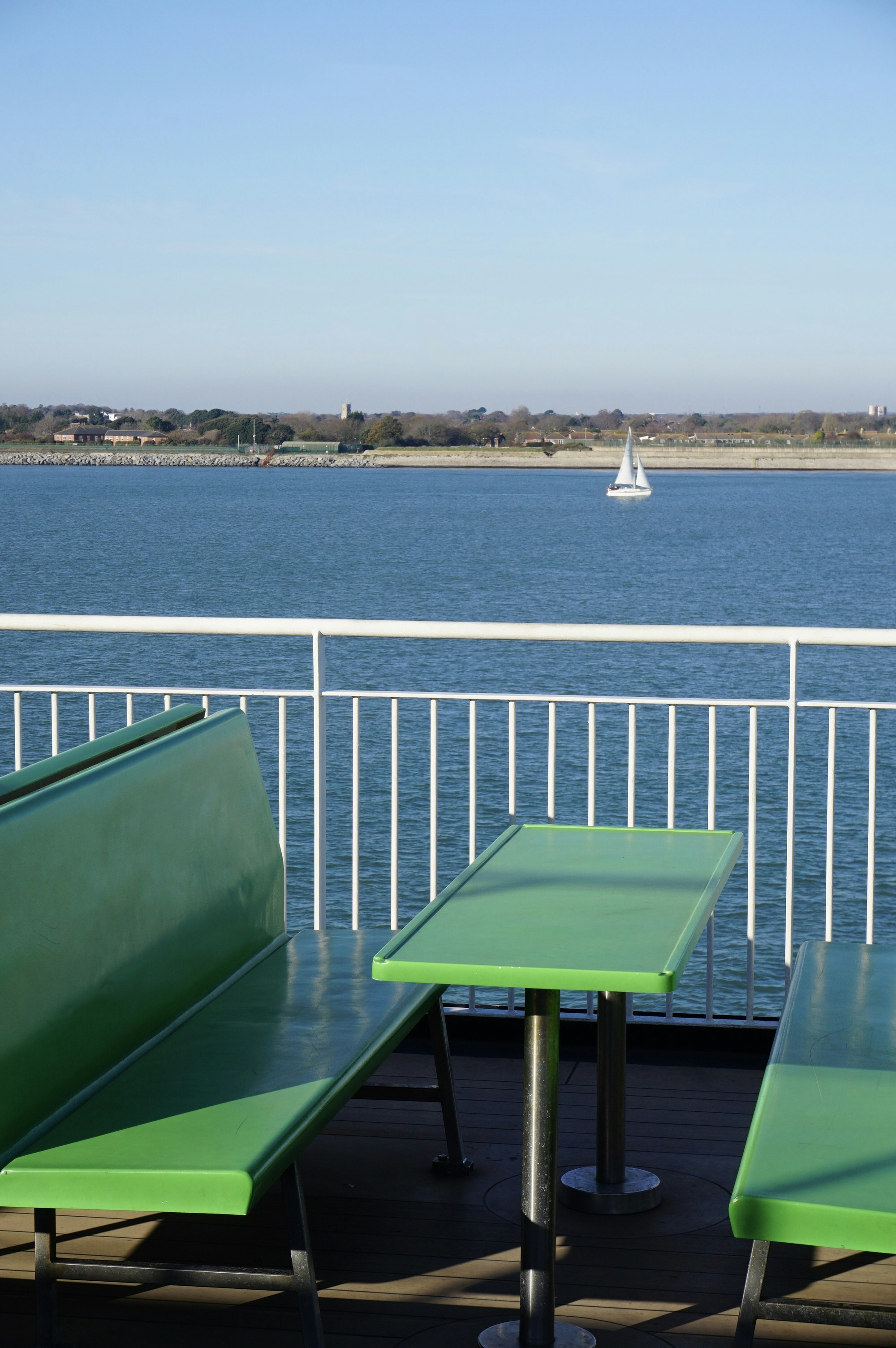 Quiet Promenade by the Sea: Green Seats Overlook a Distant Sail