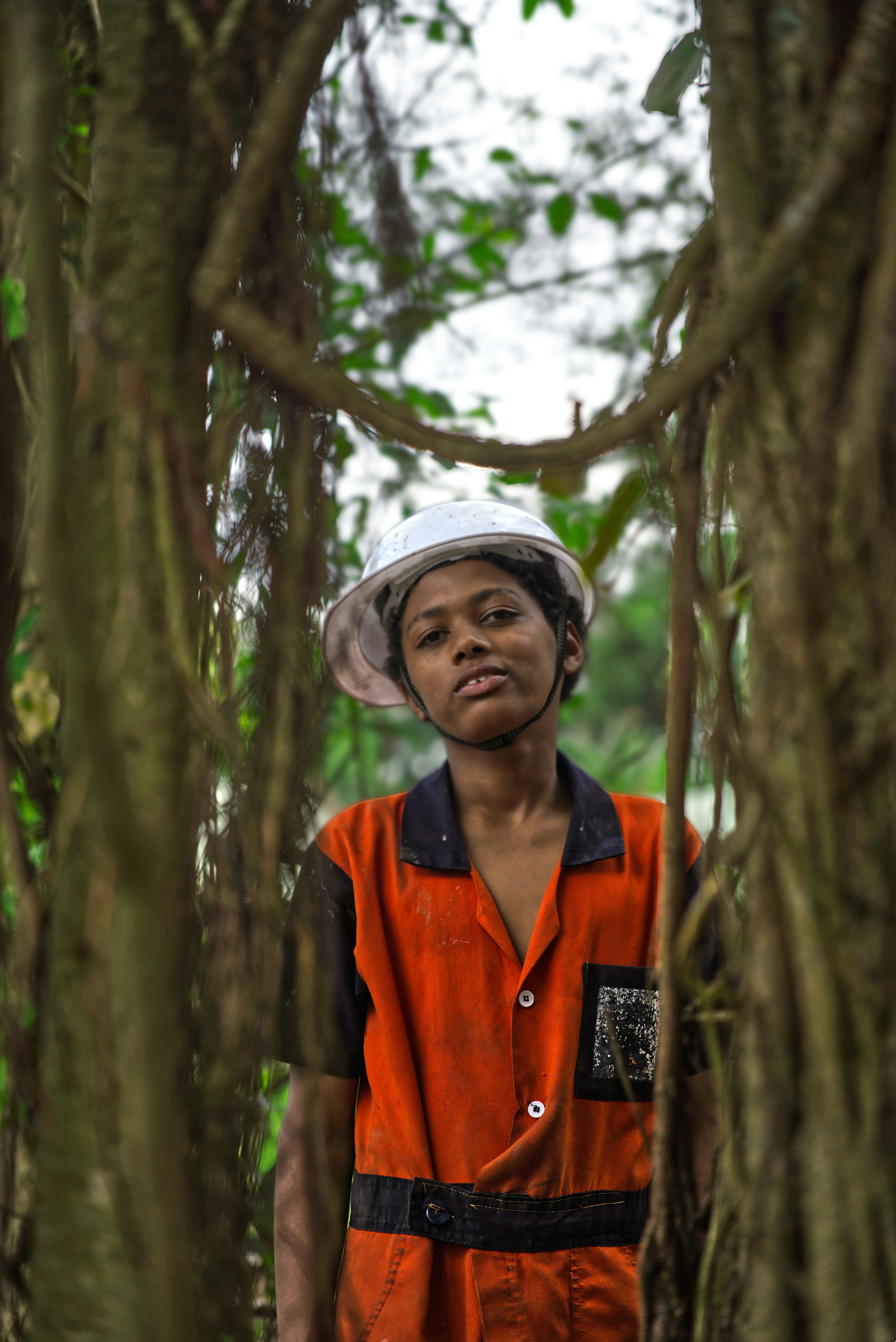 Worker in orange jumpsuit emerges from the vines under a white helmet