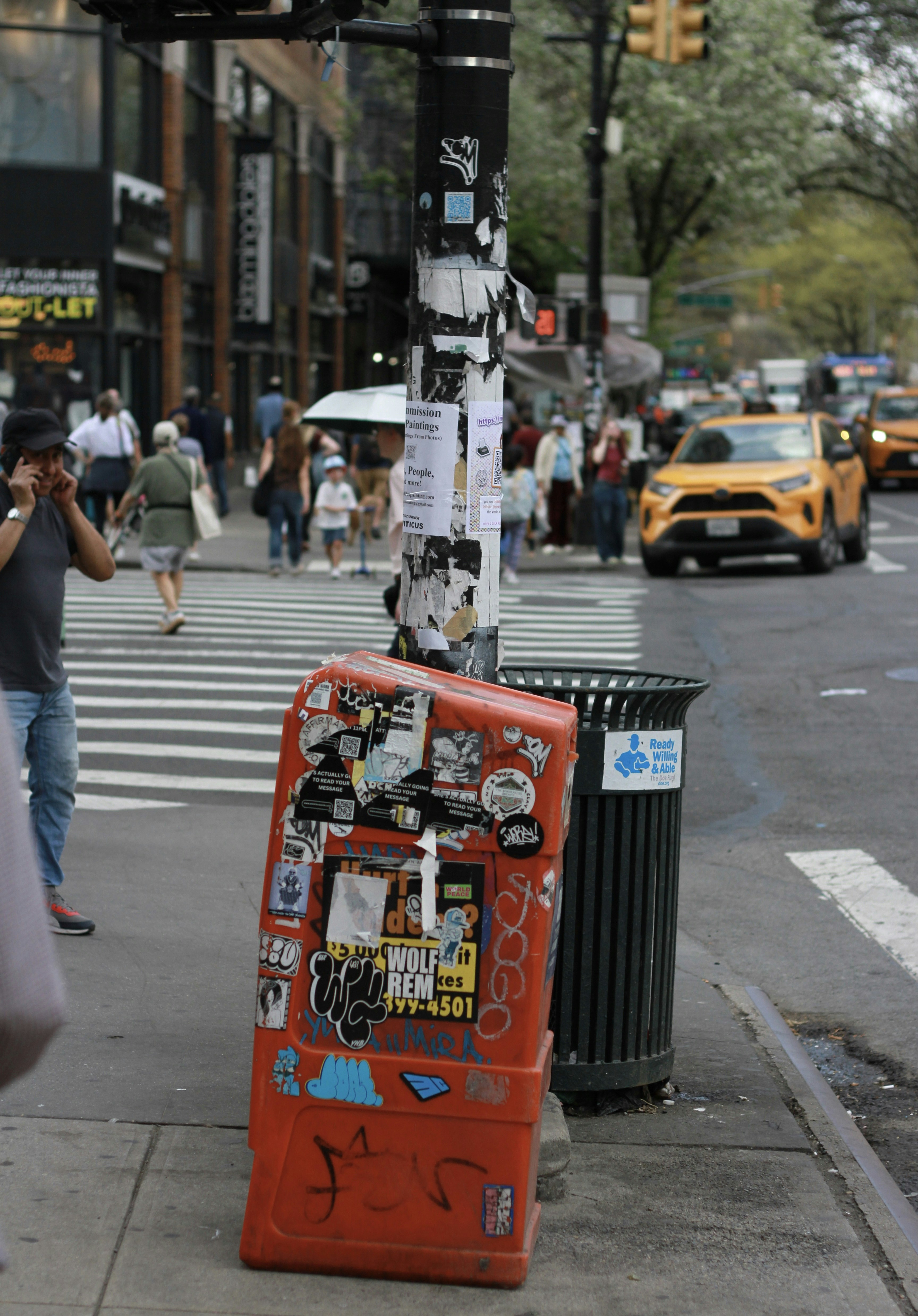 Graffiti-Scarred Street Pole and Candy-Red Newsstand in a Busy City Crosswalk
