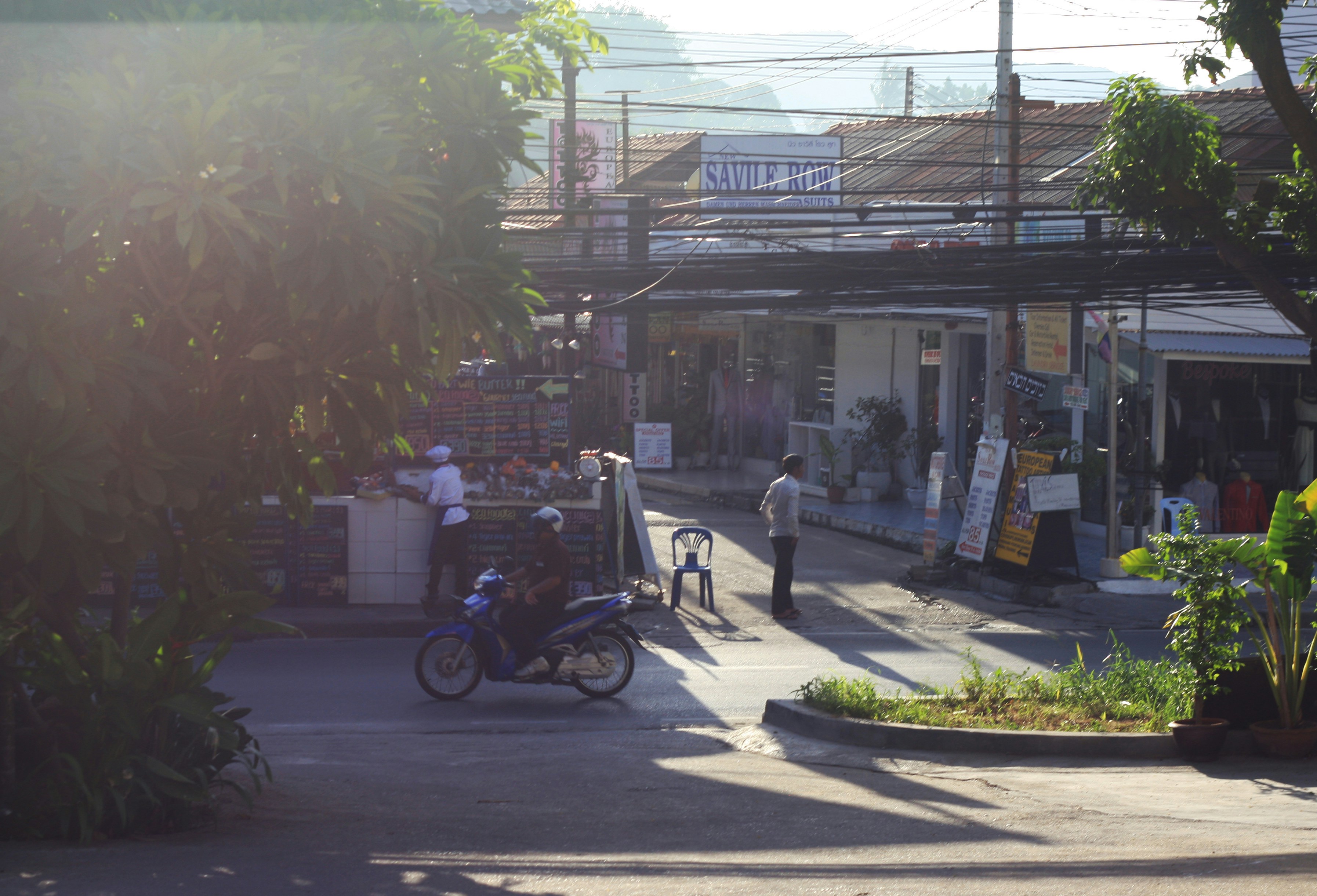 Sunlit Street Corner with Motorbike and Café in Soft Focus