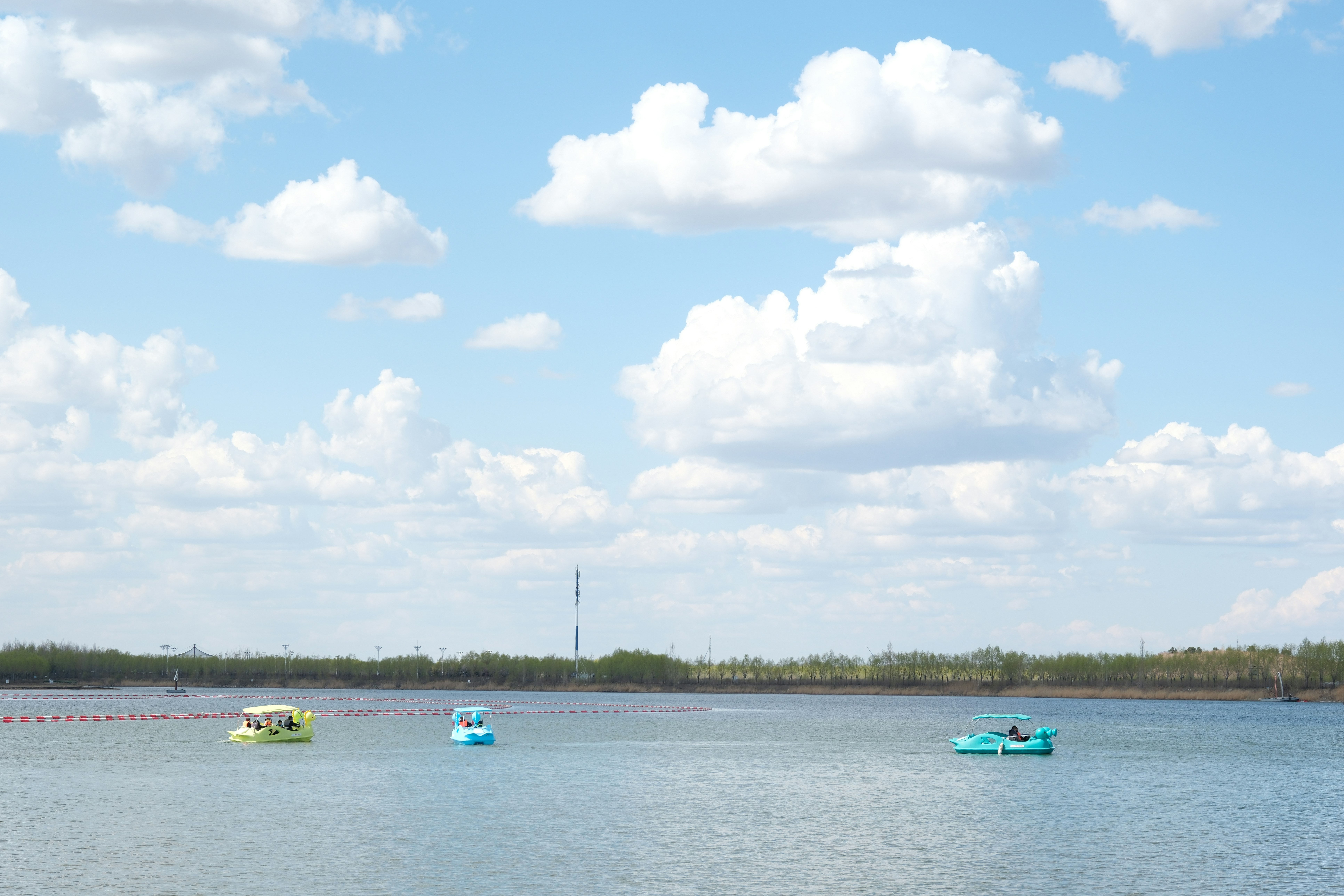 Colorful boats drift on a calm lake under a sky of puffy clouds