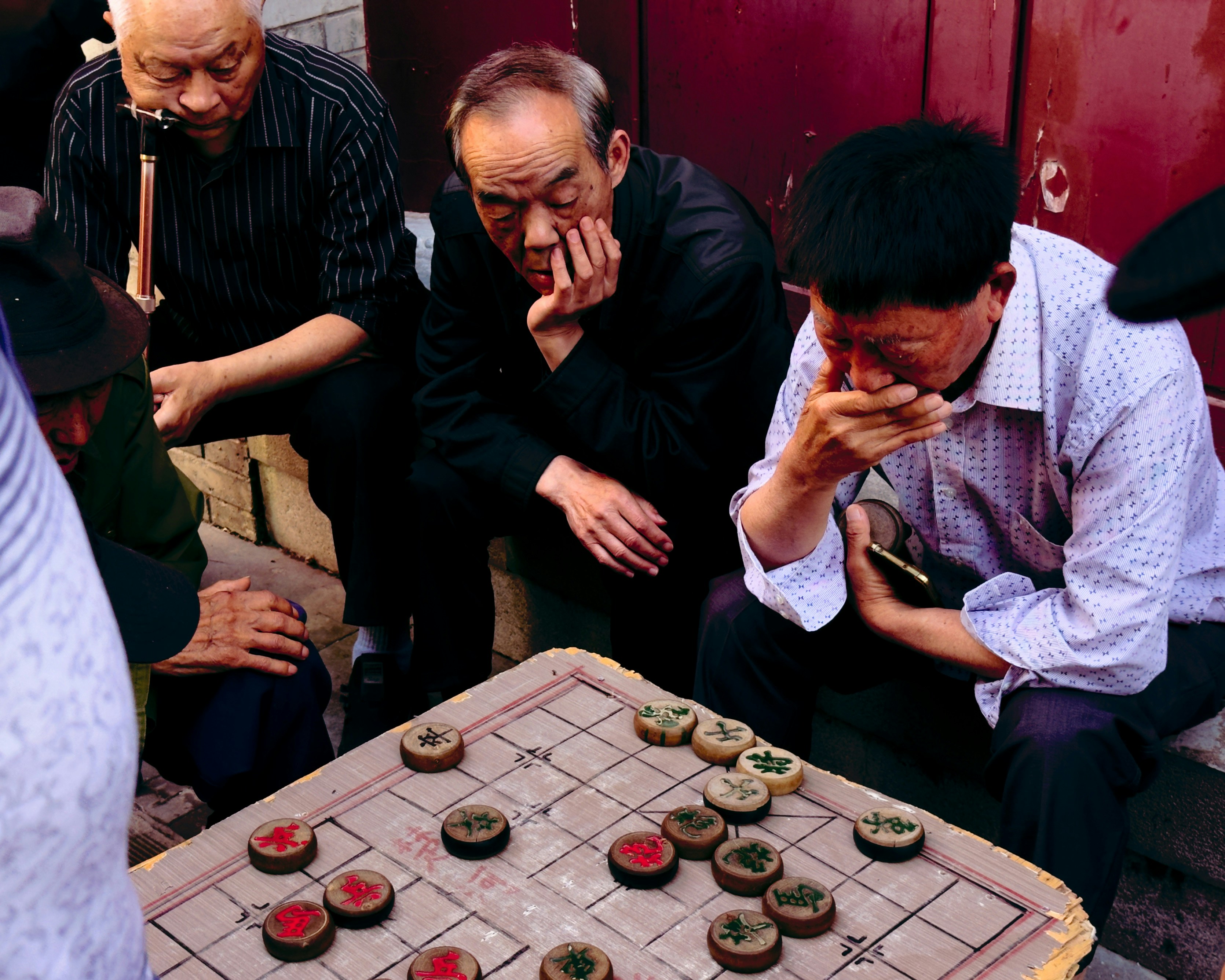 Three men in contemplation around a carved board game on a dusty street