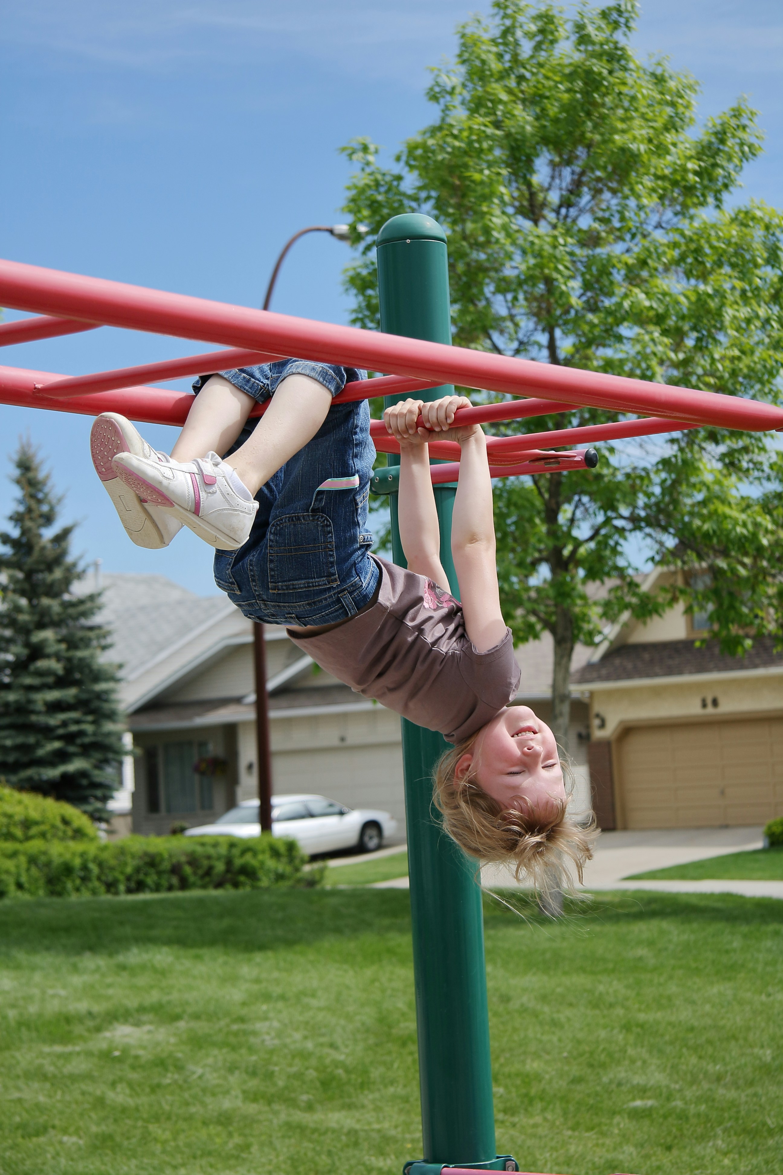 Upside-Down Playground: a girl swinging on red bars against a sunny suburb