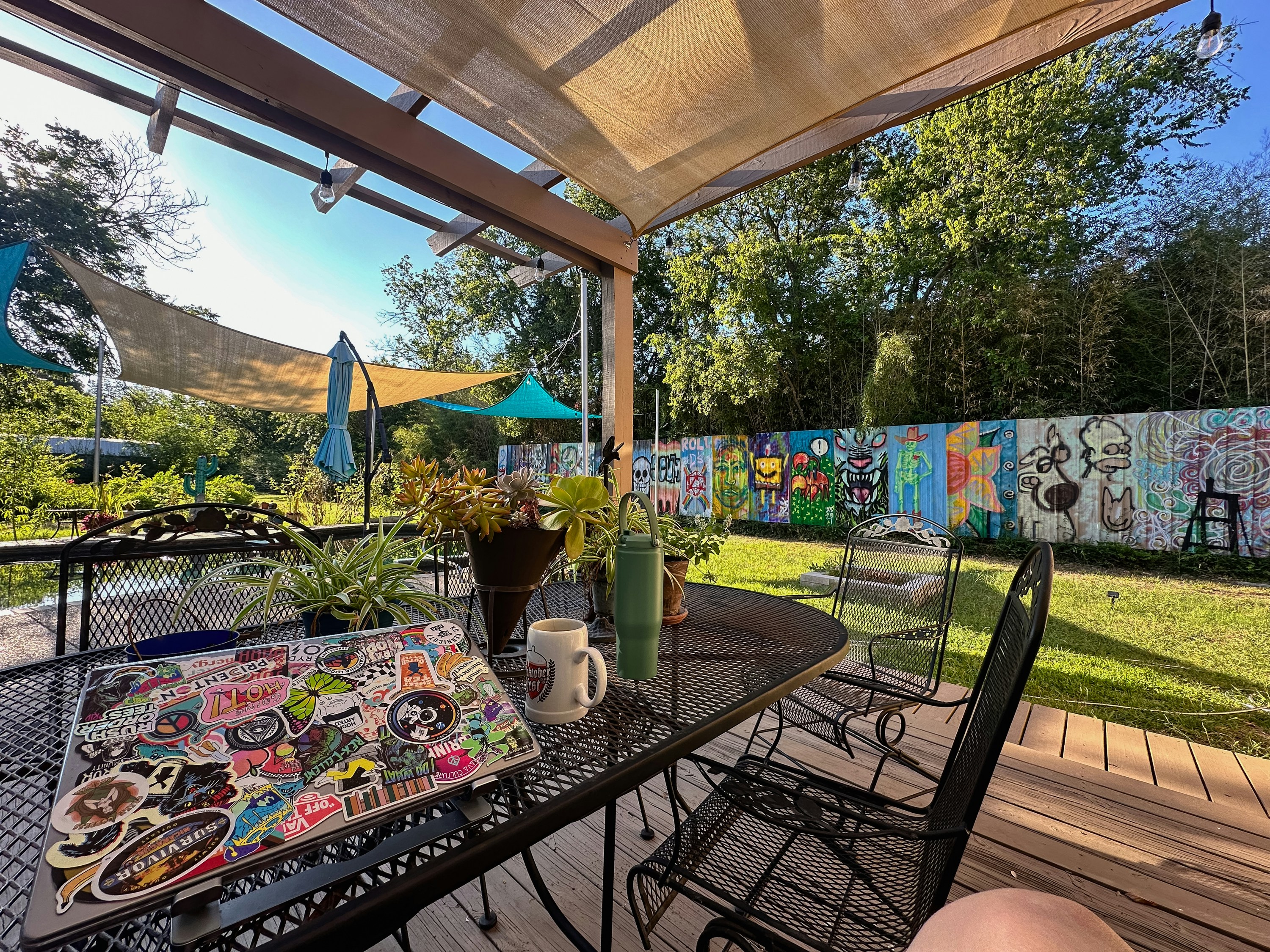 Stickered Laptop on a Sunlit Outdoor Patio with Colorful Fence Art