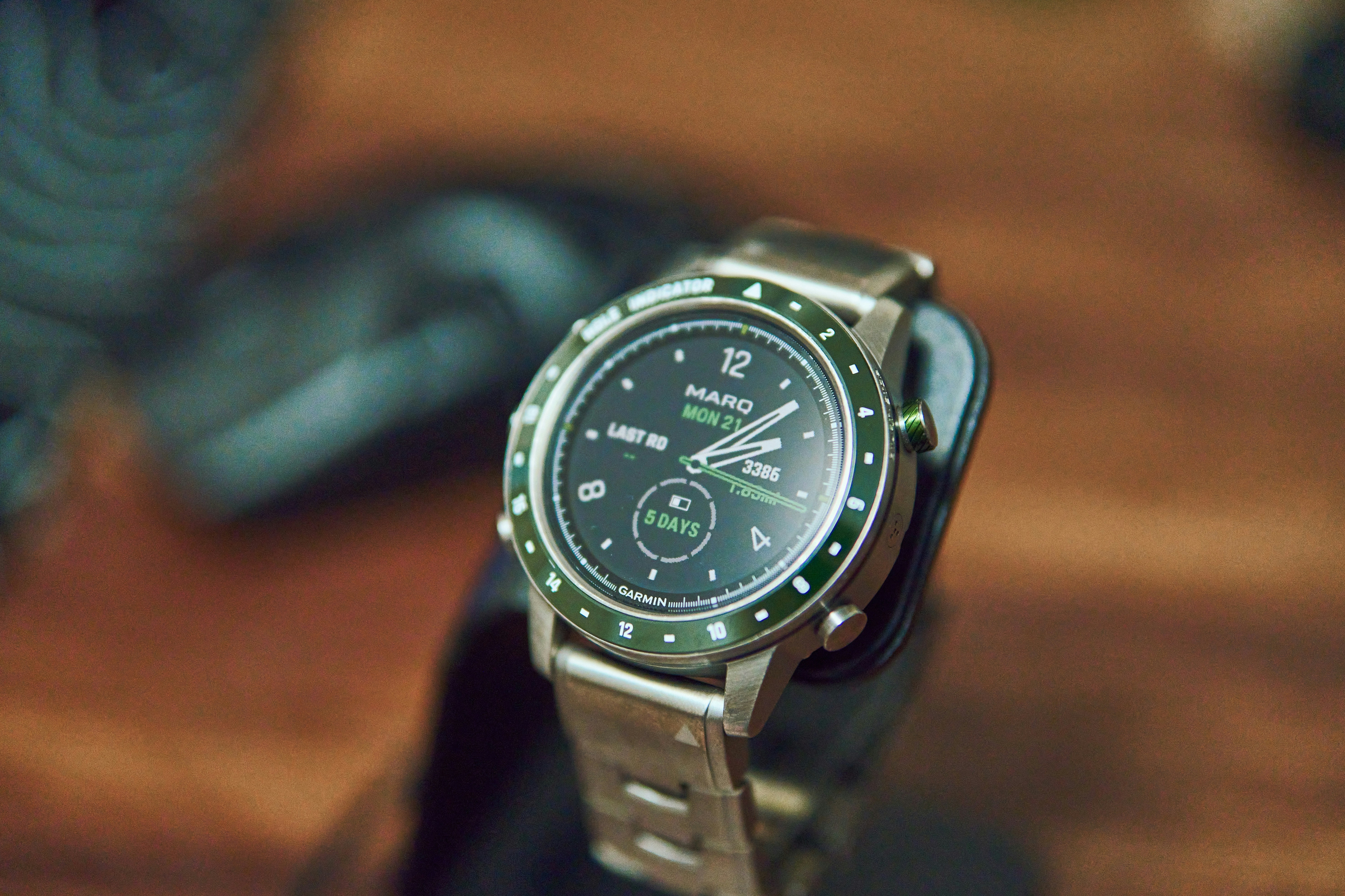 Close-up of a metallic wristwatch on a stand, with a blurred wooden background; showcases a detailed dial and metallic strap.